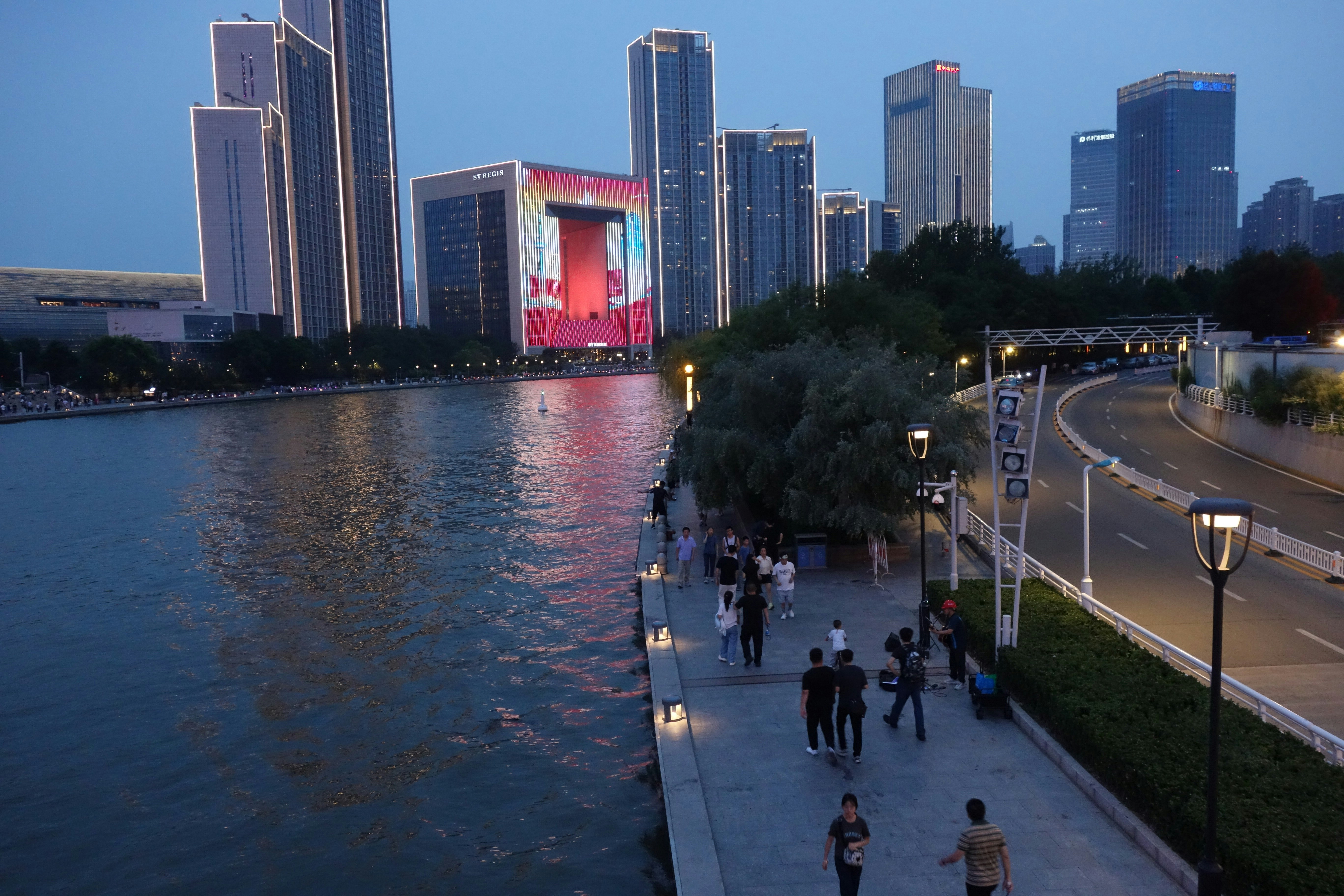Dusk along the Riverside Promenade: Glass Towers and People in Evening Blue