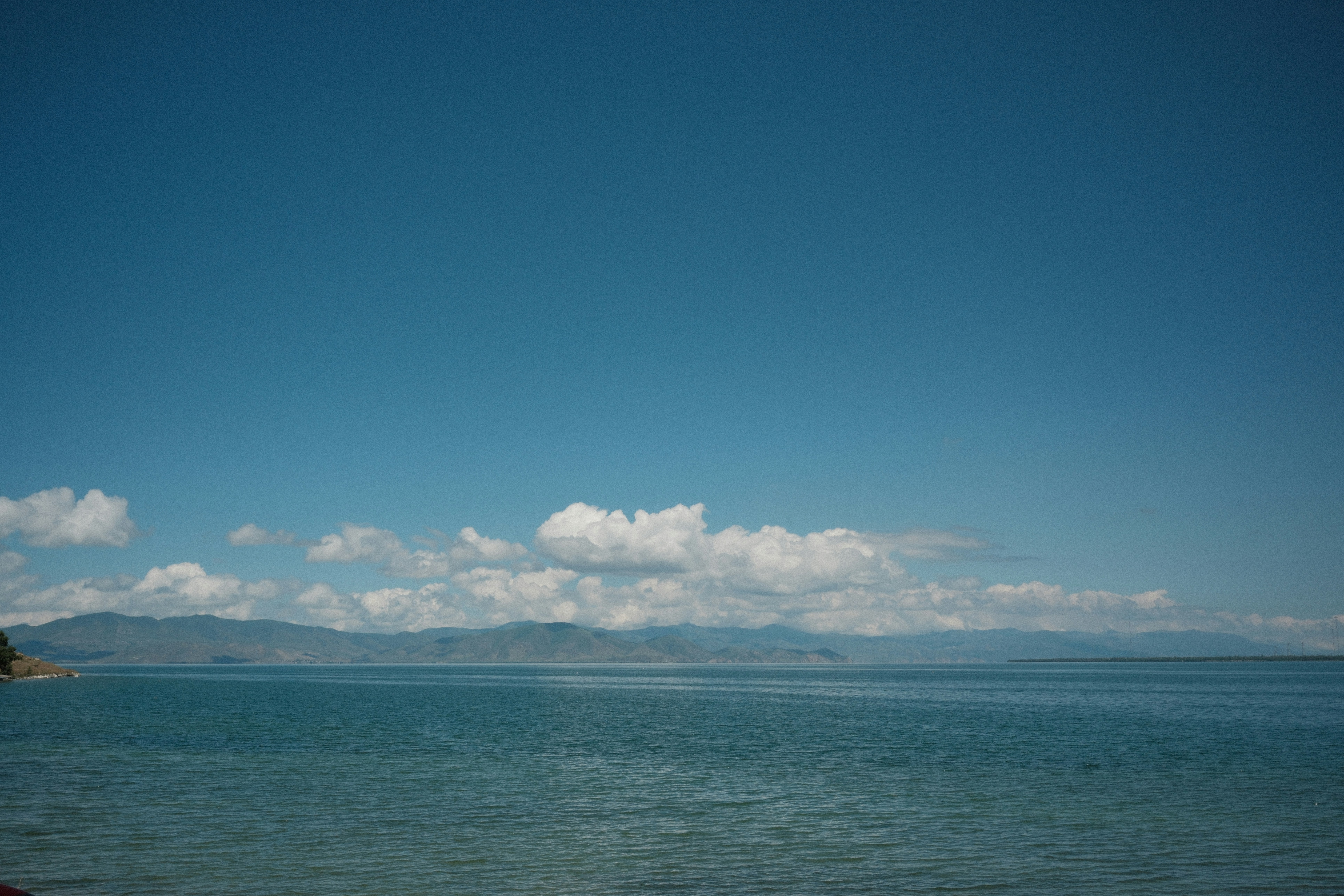 Calm lake with a clear blue sky and distant clouds; tranquil shoreline mood, captured as a wide landscape.