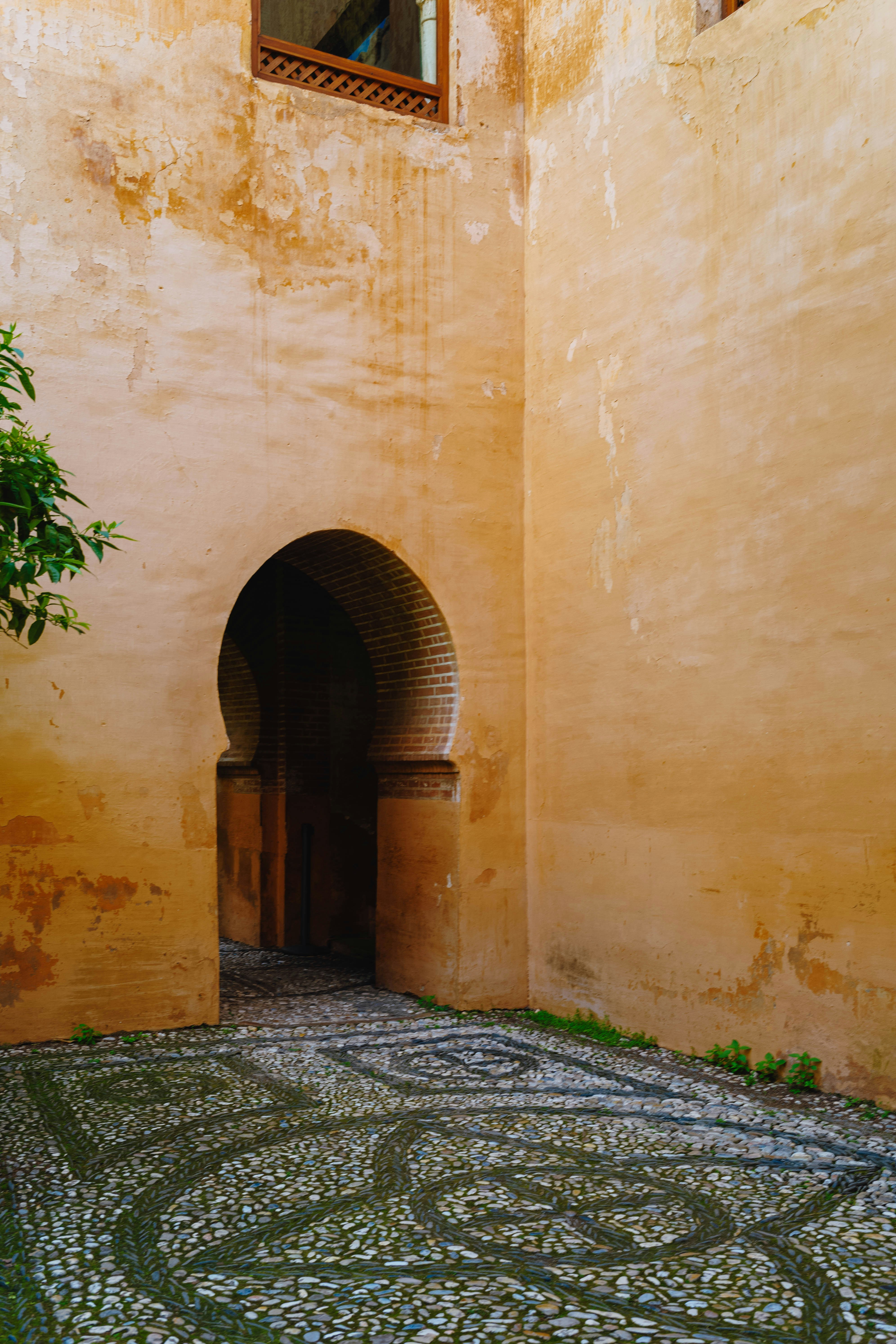 Archway in Sunlit Courtyard: A Warm Allure of Stone and Patterned Cobblestones