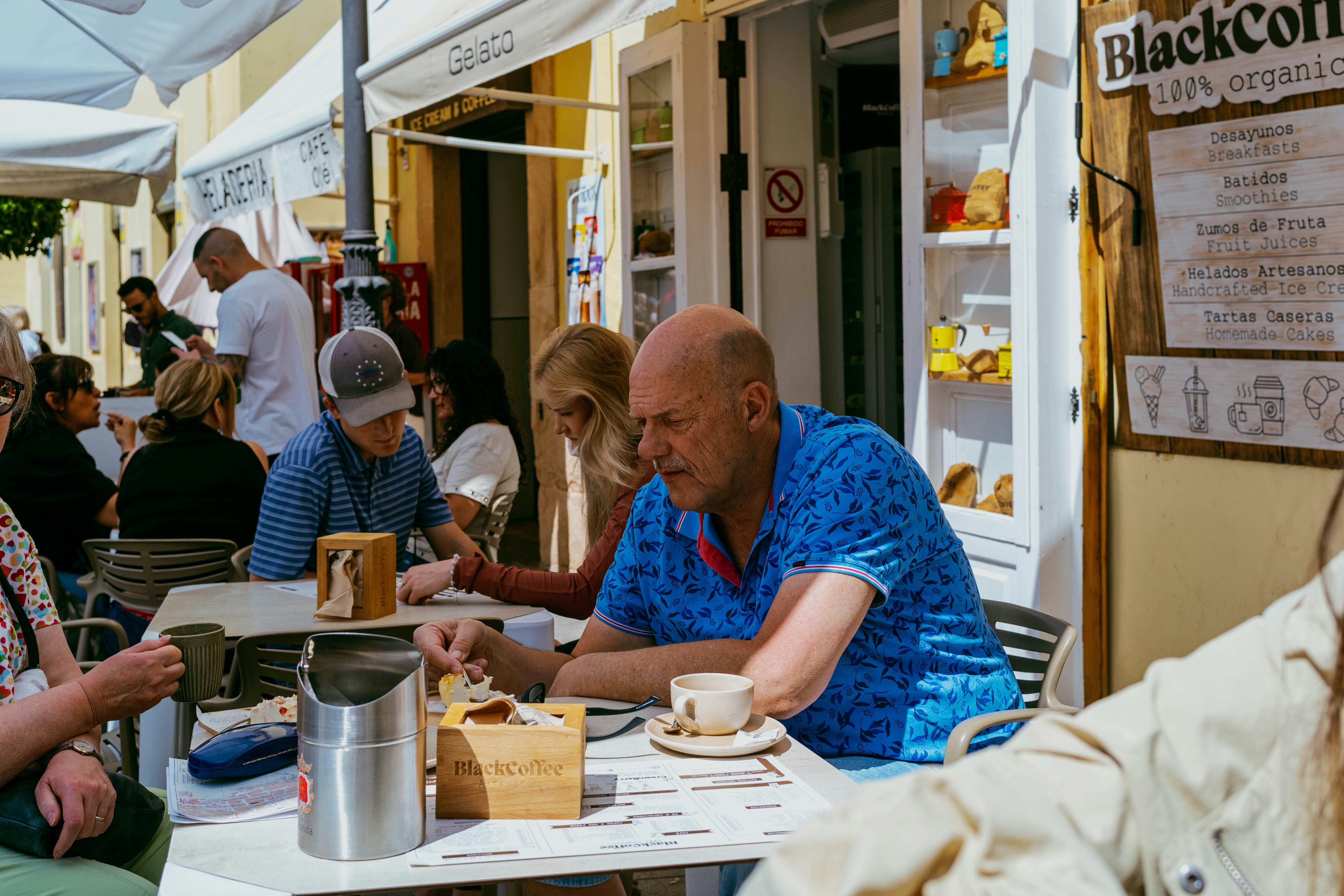 Blue Shirt Focus: A Quiet Café Moment Amidst a Bustling Street