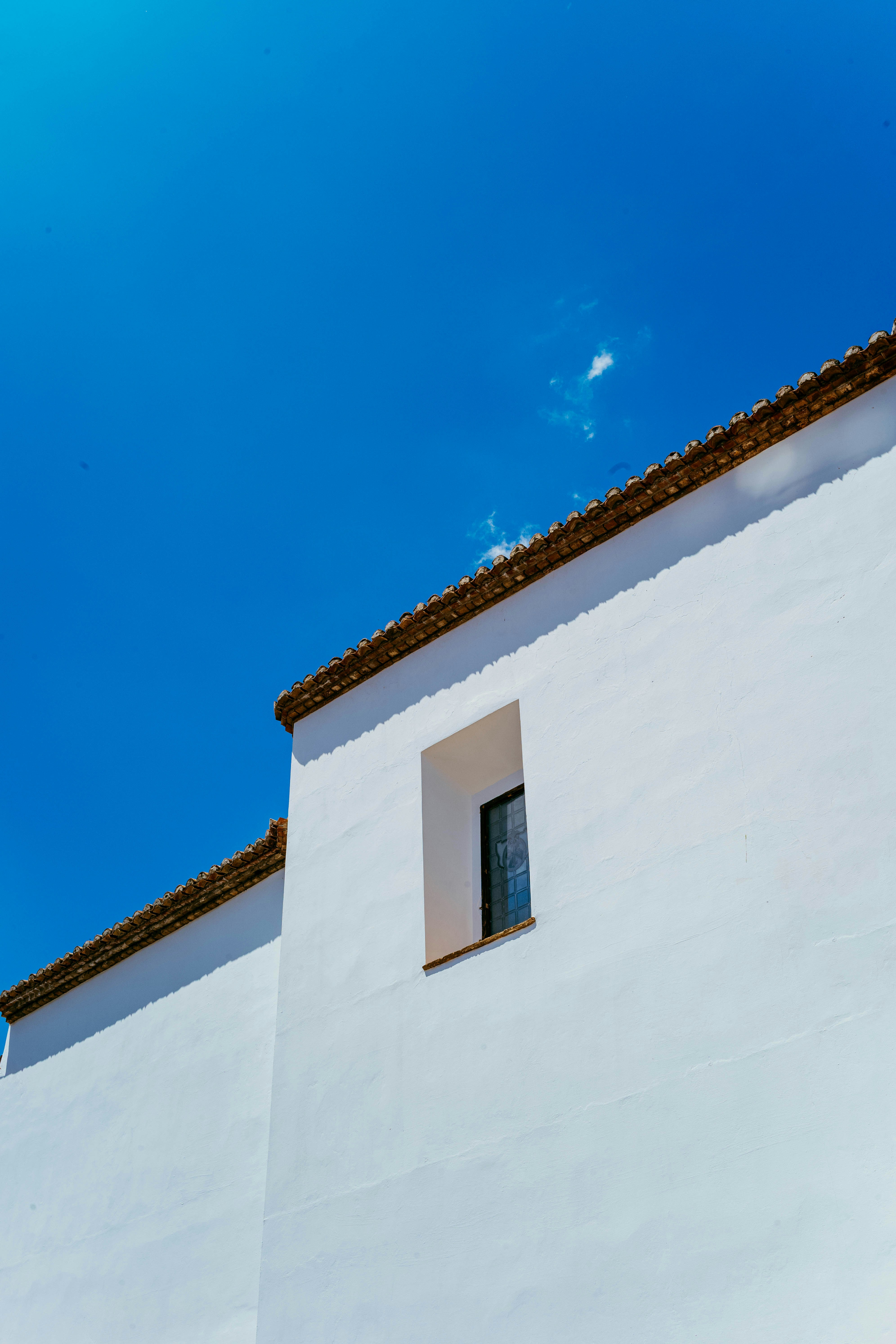 Clean white wall with a single window under a bright blue sky, emphasizing architectural minimalism and strong contrast.