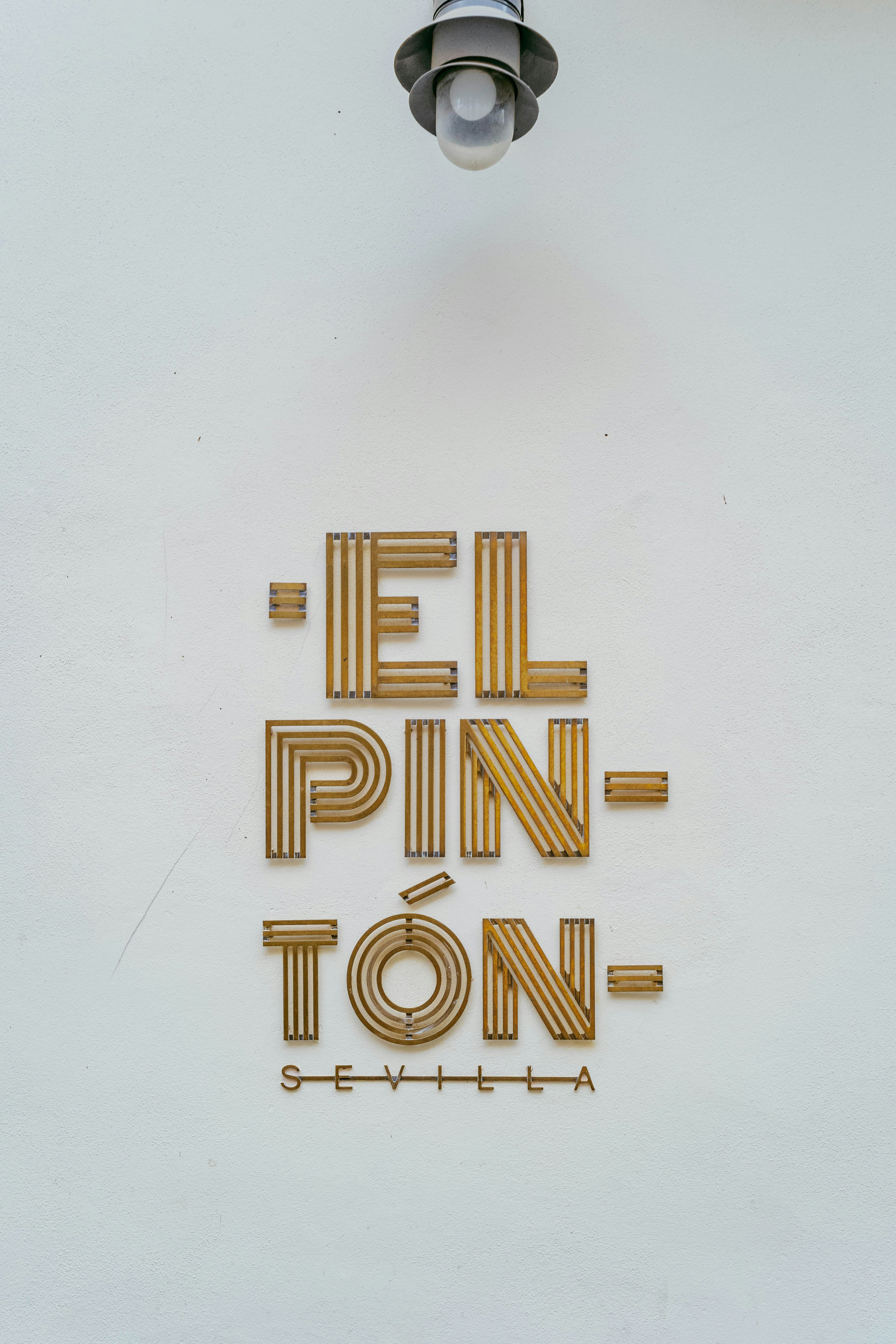 Copper Letters on White Wall: Sevilla Signage Embraced by Soft Light