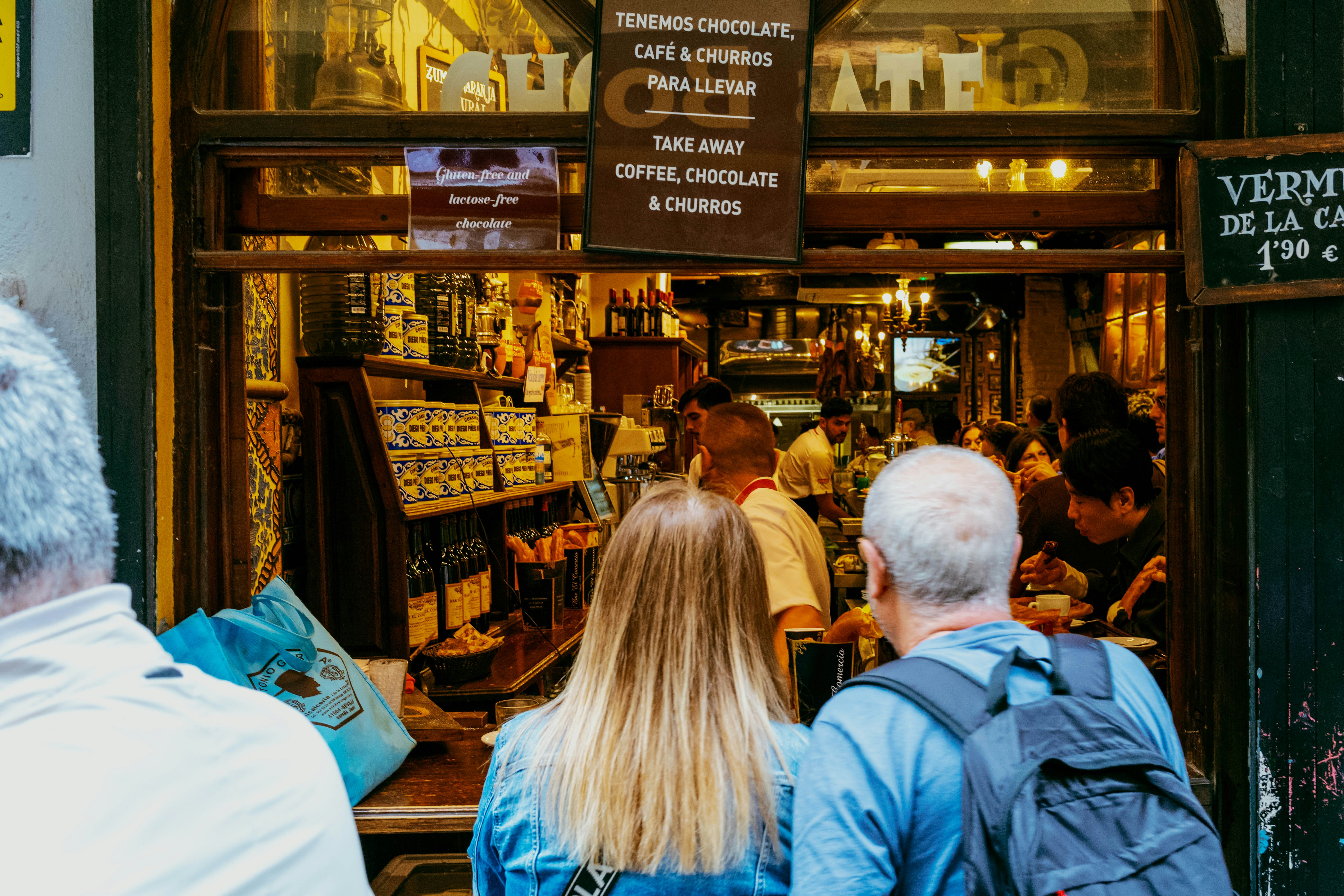 Bustling storefront: a couple in the foreground leads into a warm, chaotic café-haberdashery interior