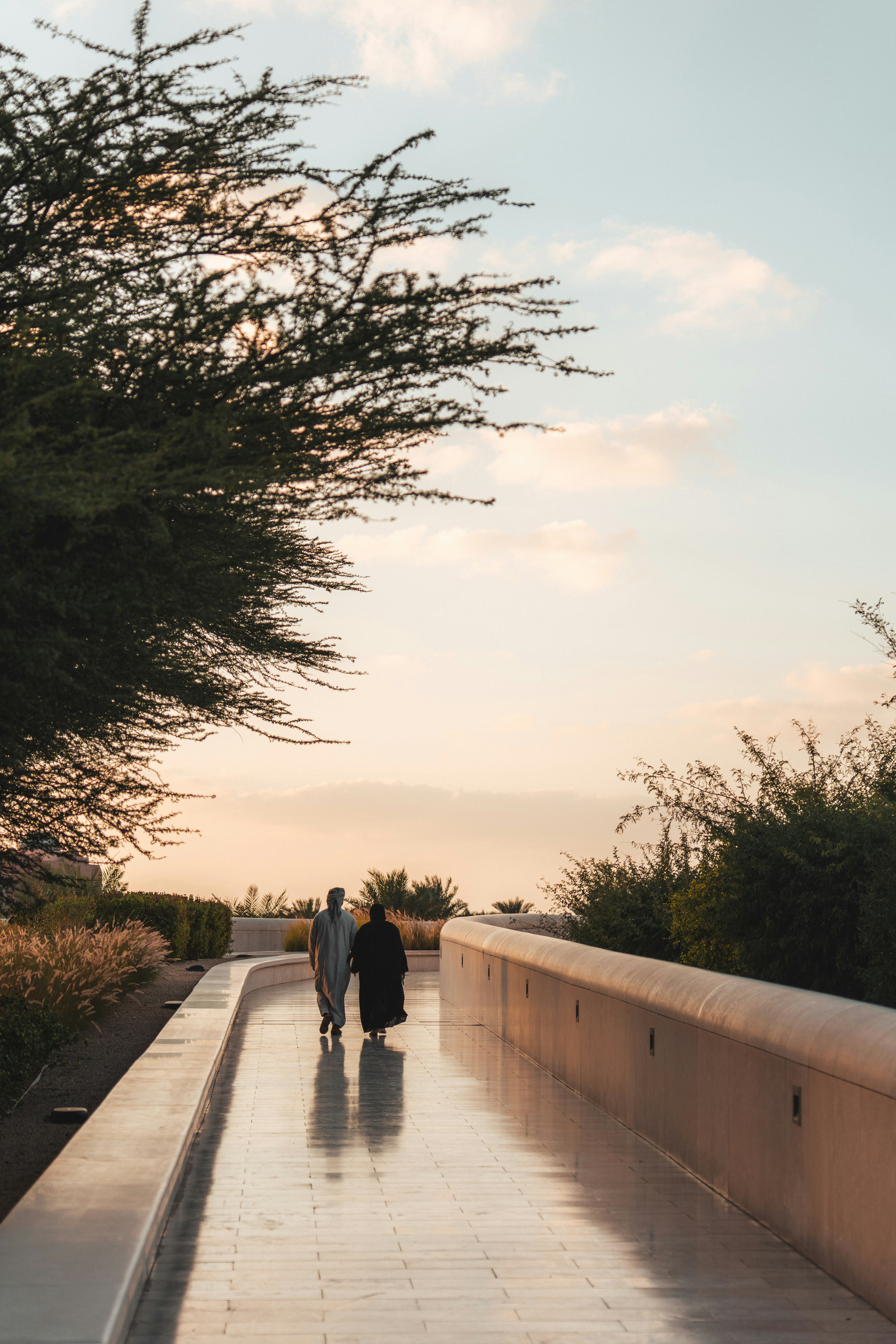 Two Figures Walk the Reflective Riverside Path at Sunset