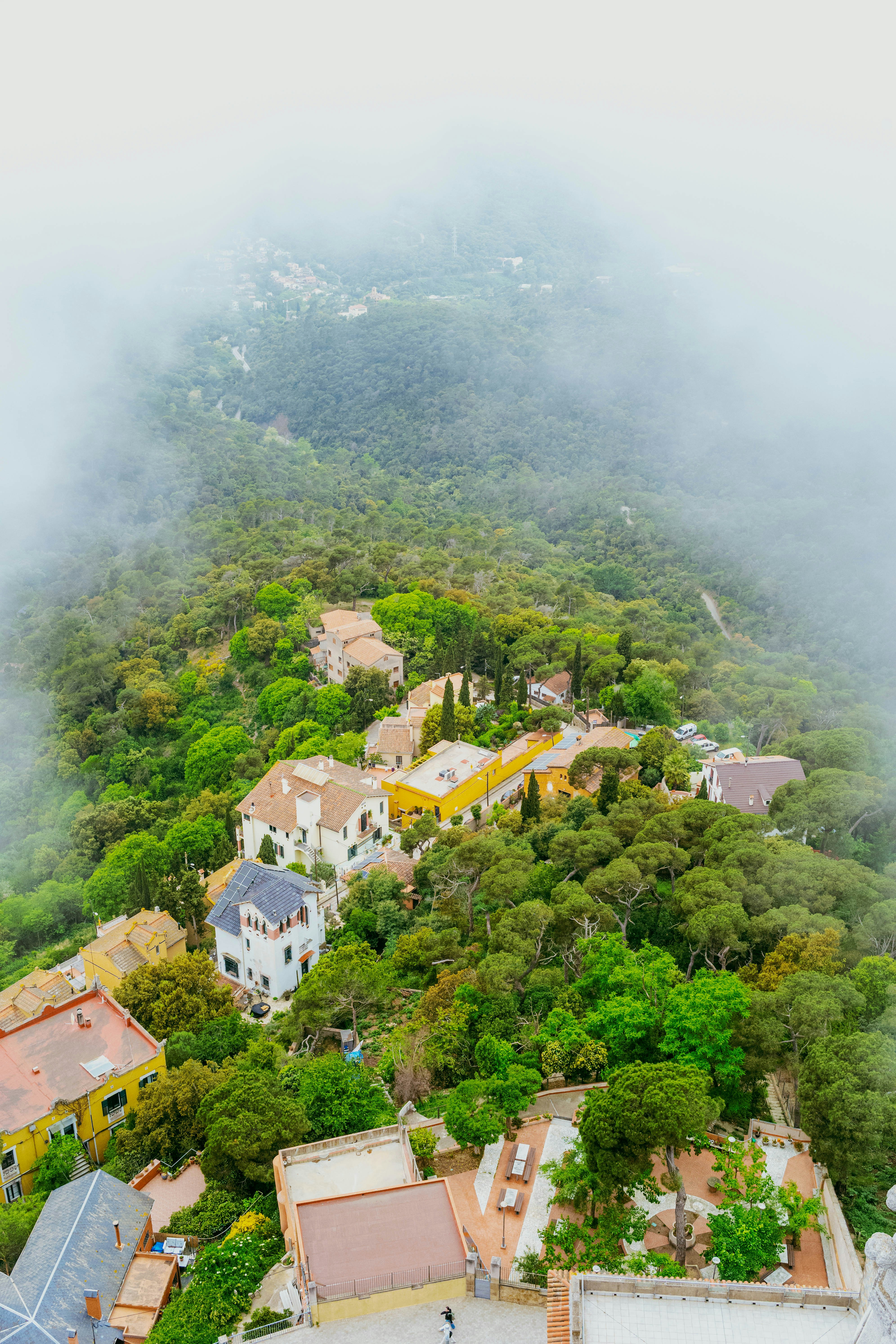 Aerial Village Veil: Houses Nestled in Verdant Hills Shrouded by Mist