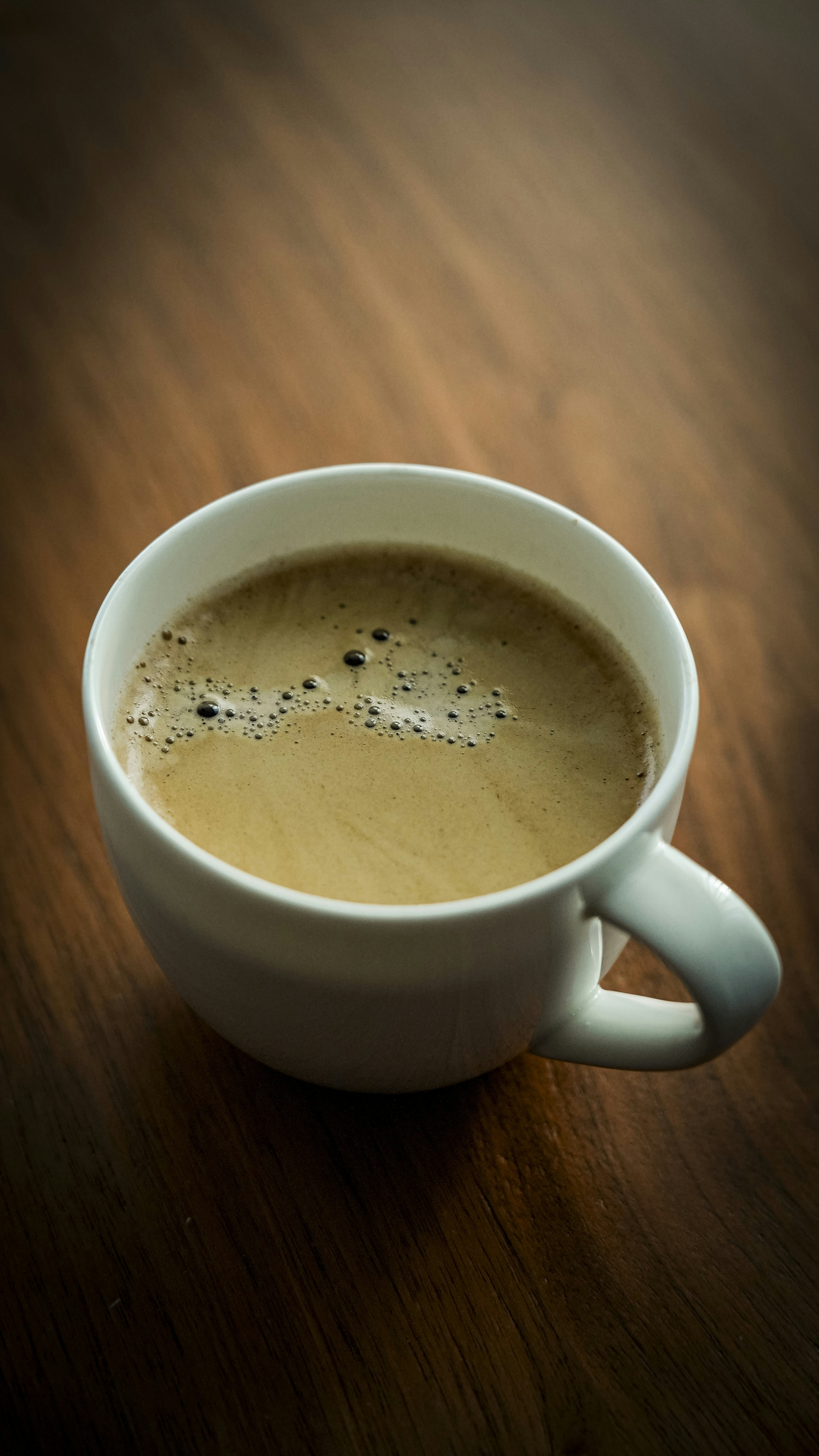 Fresh espresso in a white cup on a wooden background.