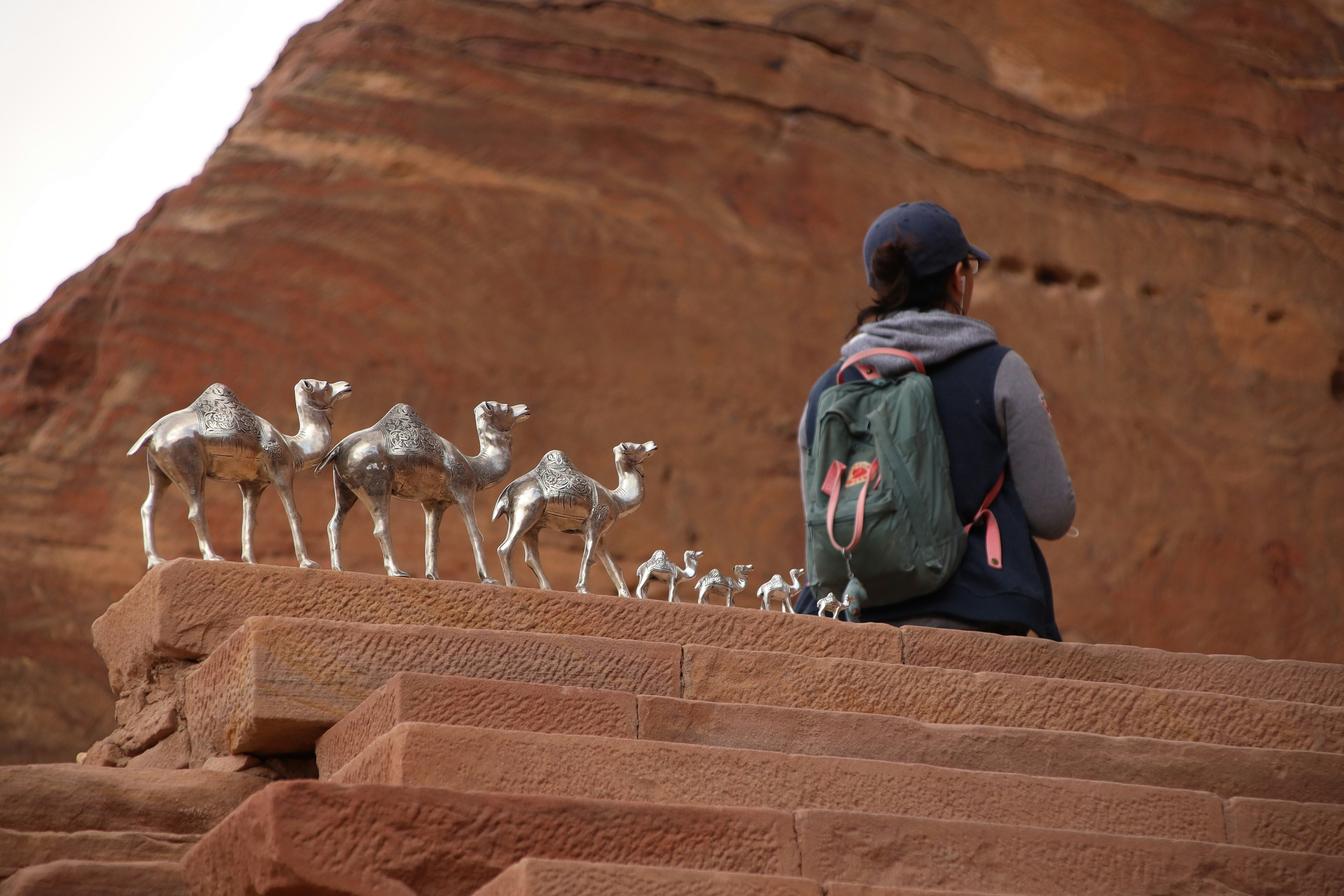 Traveler with a Row of Desert Camels Against Rugged Red Cliffs