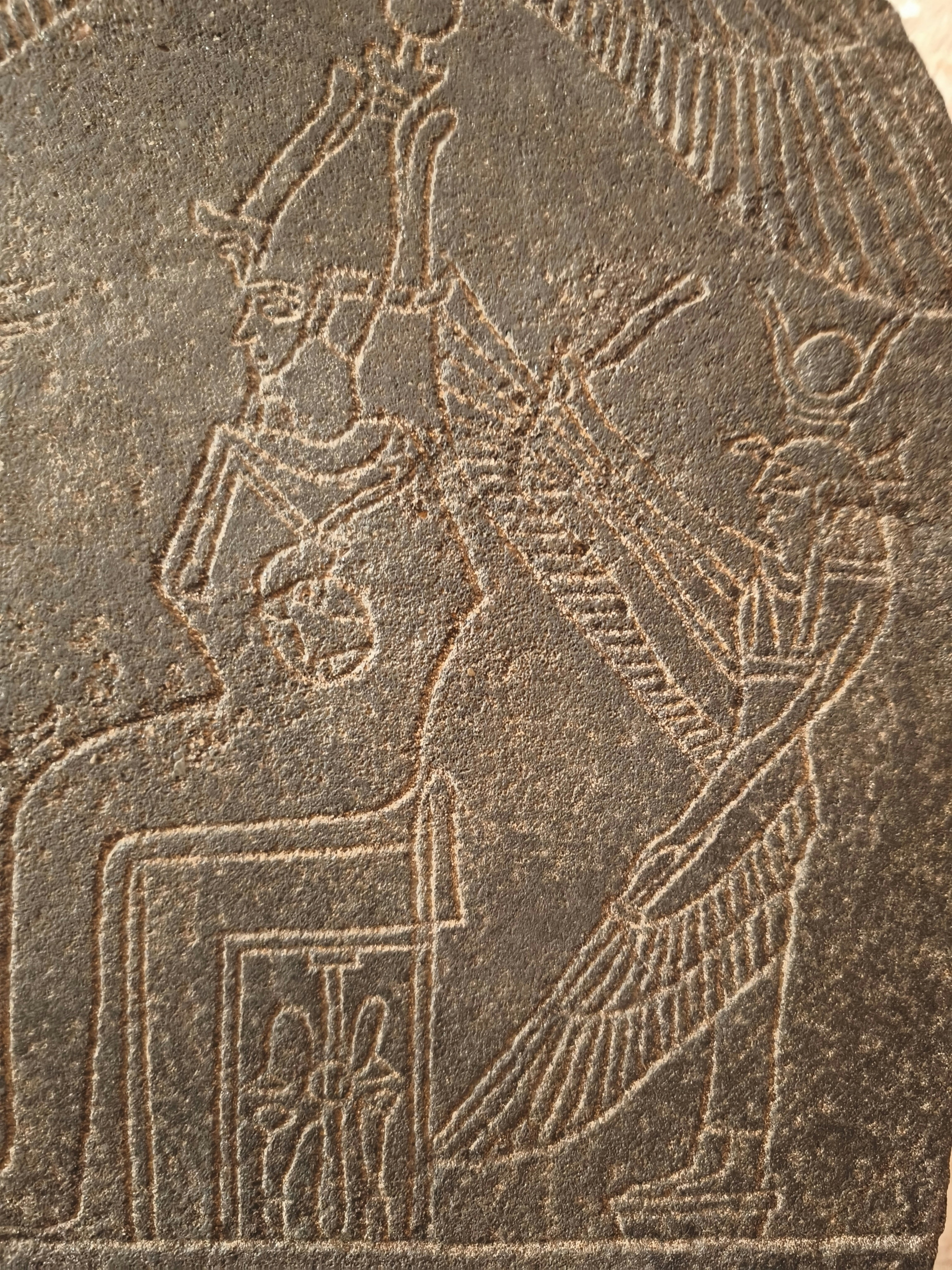 Bas-relief carving showing a seated figure and a winged deity or warrior, with an animal motif inset. The composition emphasizes anthropomorphic figures and ceremonial posture carved in stone.