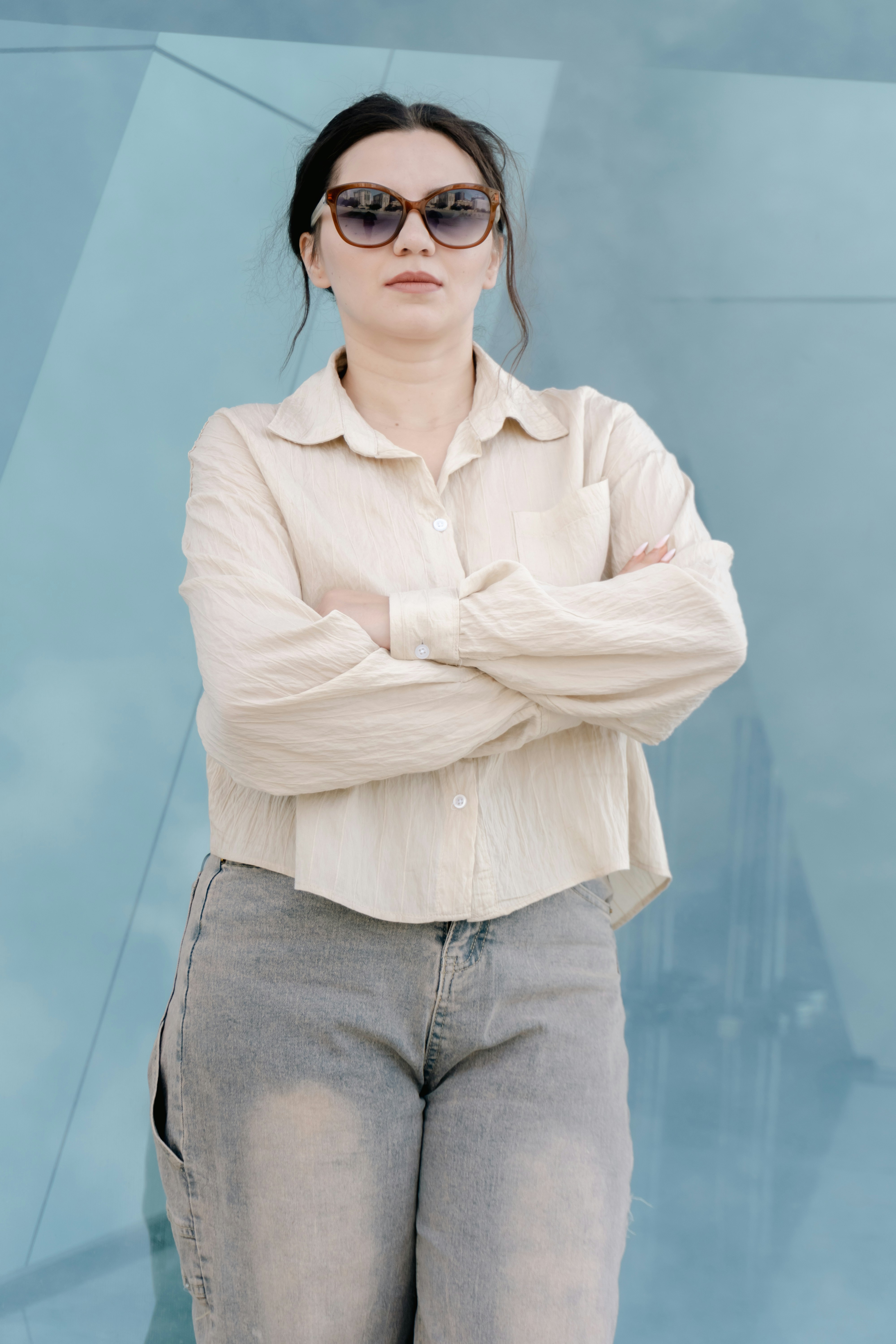 Crossed Arms, Confident Gaze Against a Glassy Blue Backdrop