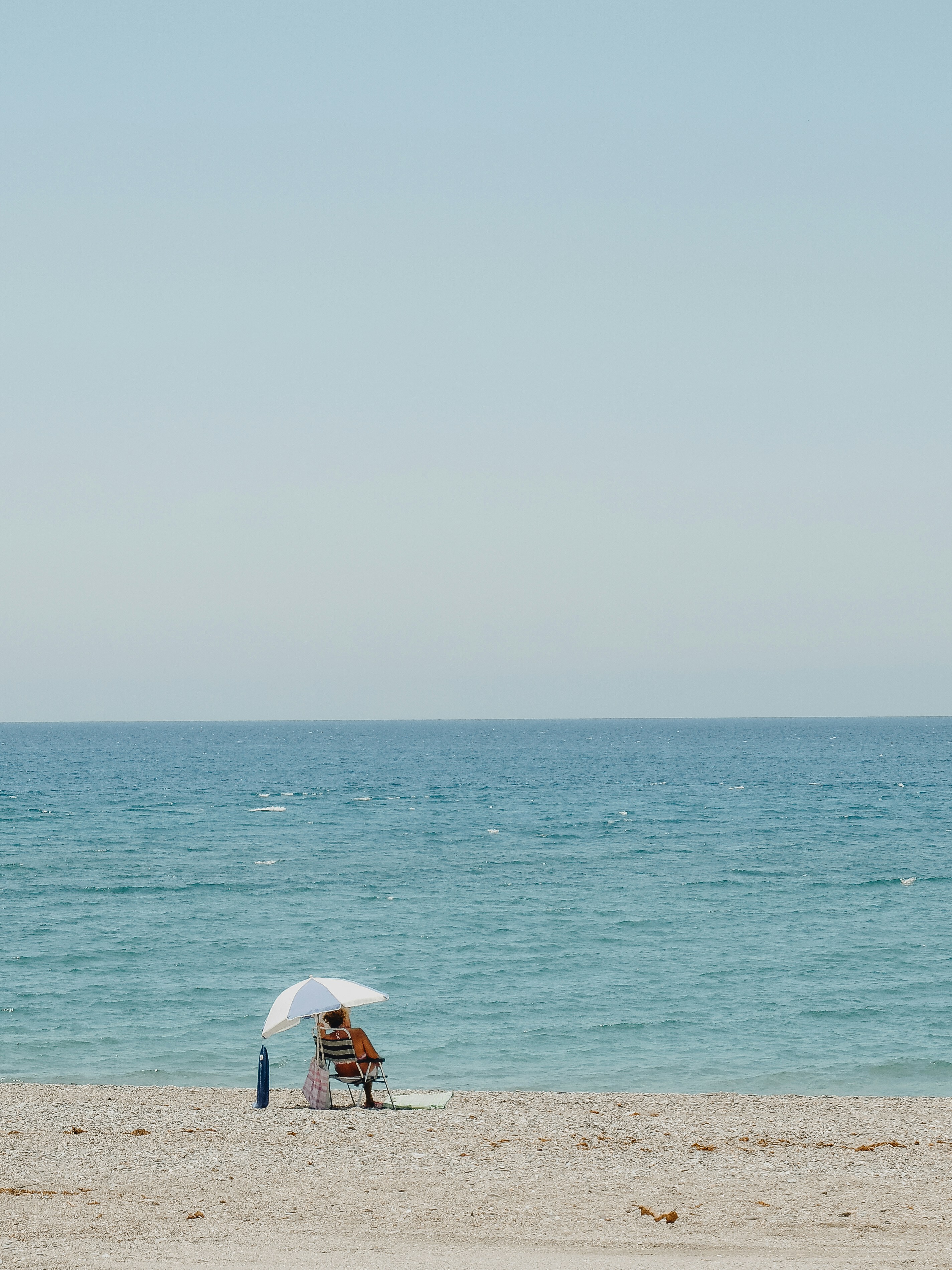 Solitary Beachside Pause: A Couple under a White Umbrella by the Calm Sea