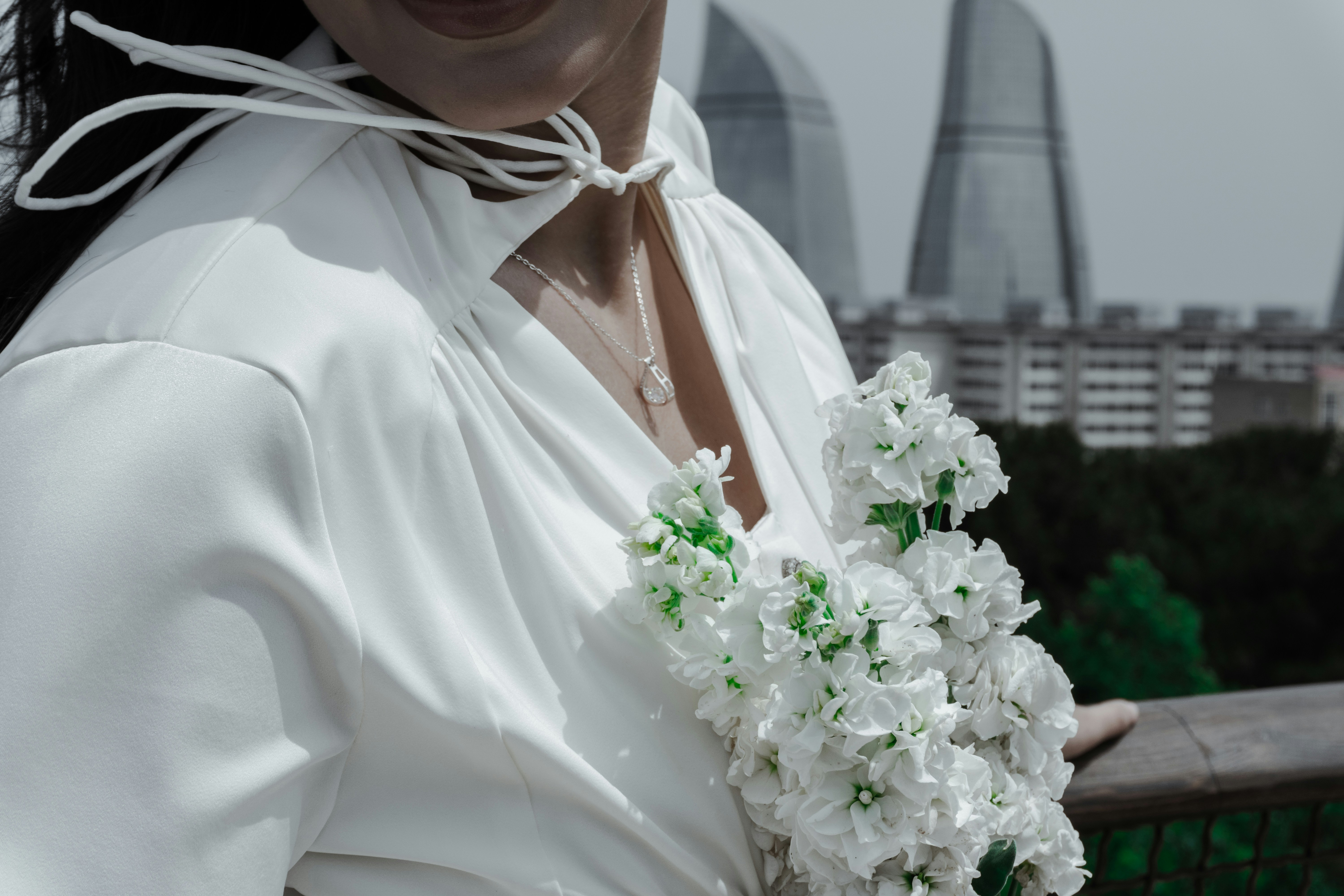 FloatingBloom: A Close-Up on White Bouquet and Neckline Amid Urban Panorama