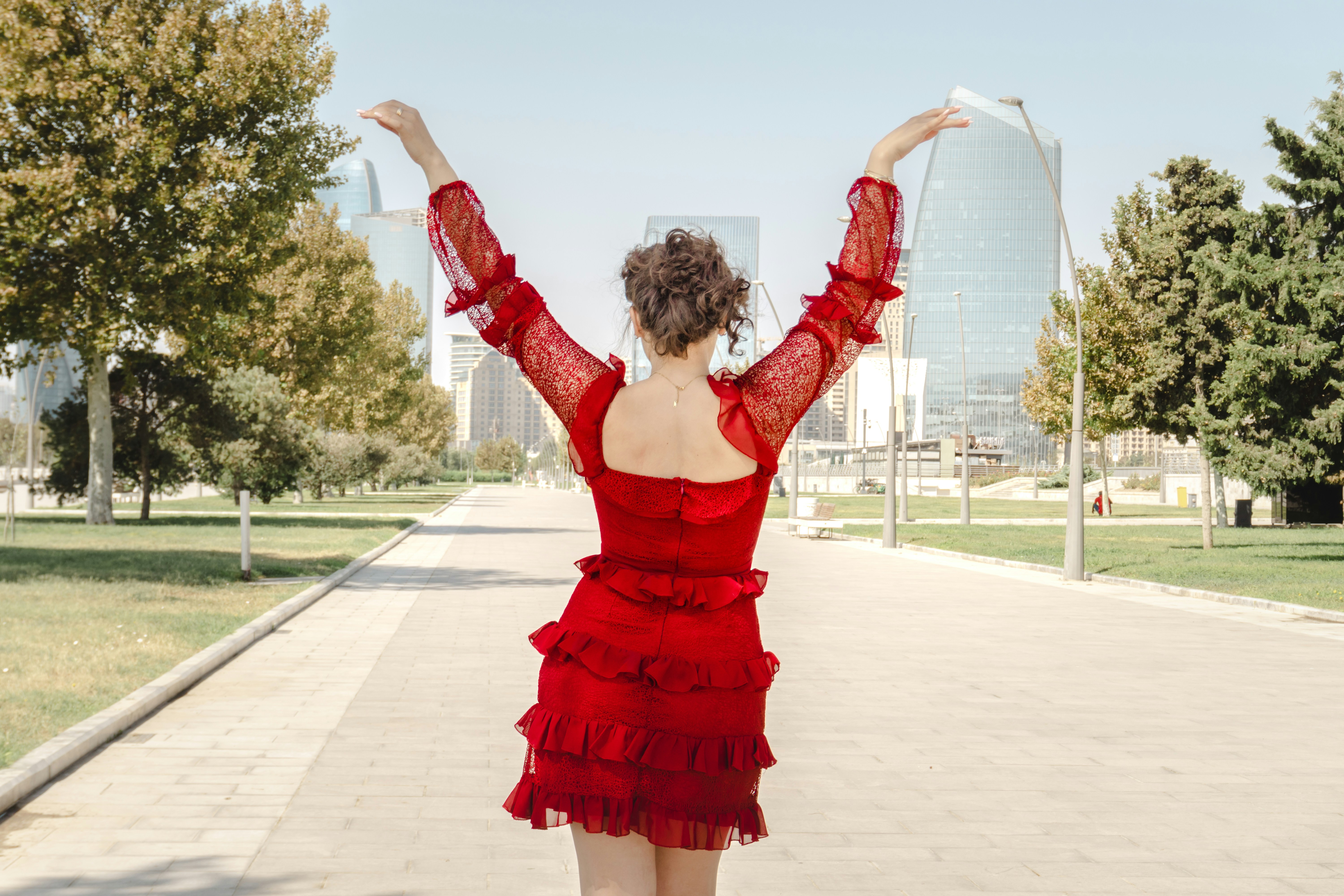 Woman in red dress raising arms outdoors on a path