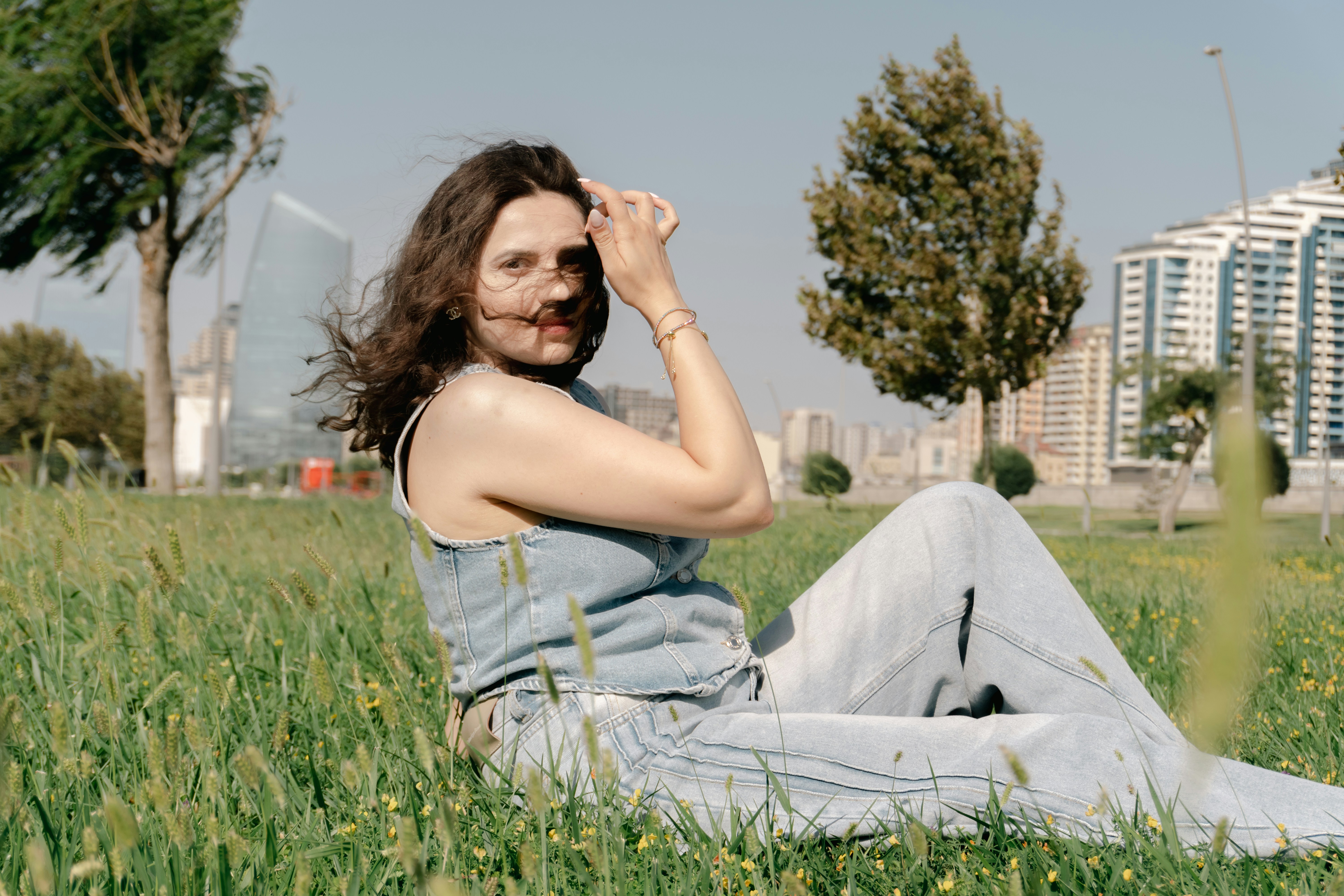Sunlit Quiet: A Woman Reclines in a Field with Urban Skyline