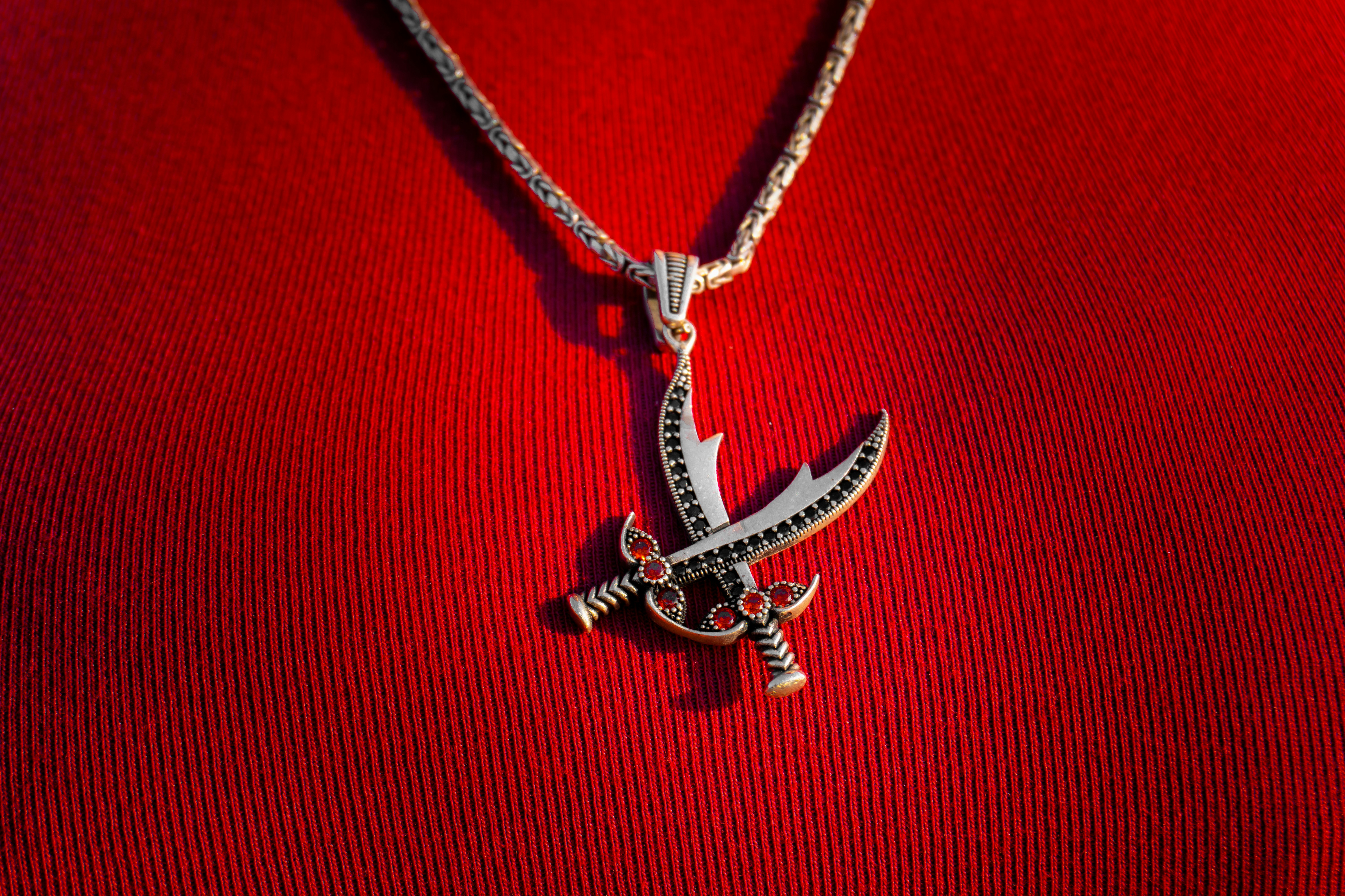 Silver necklace with crossed sword pendant on a red background.