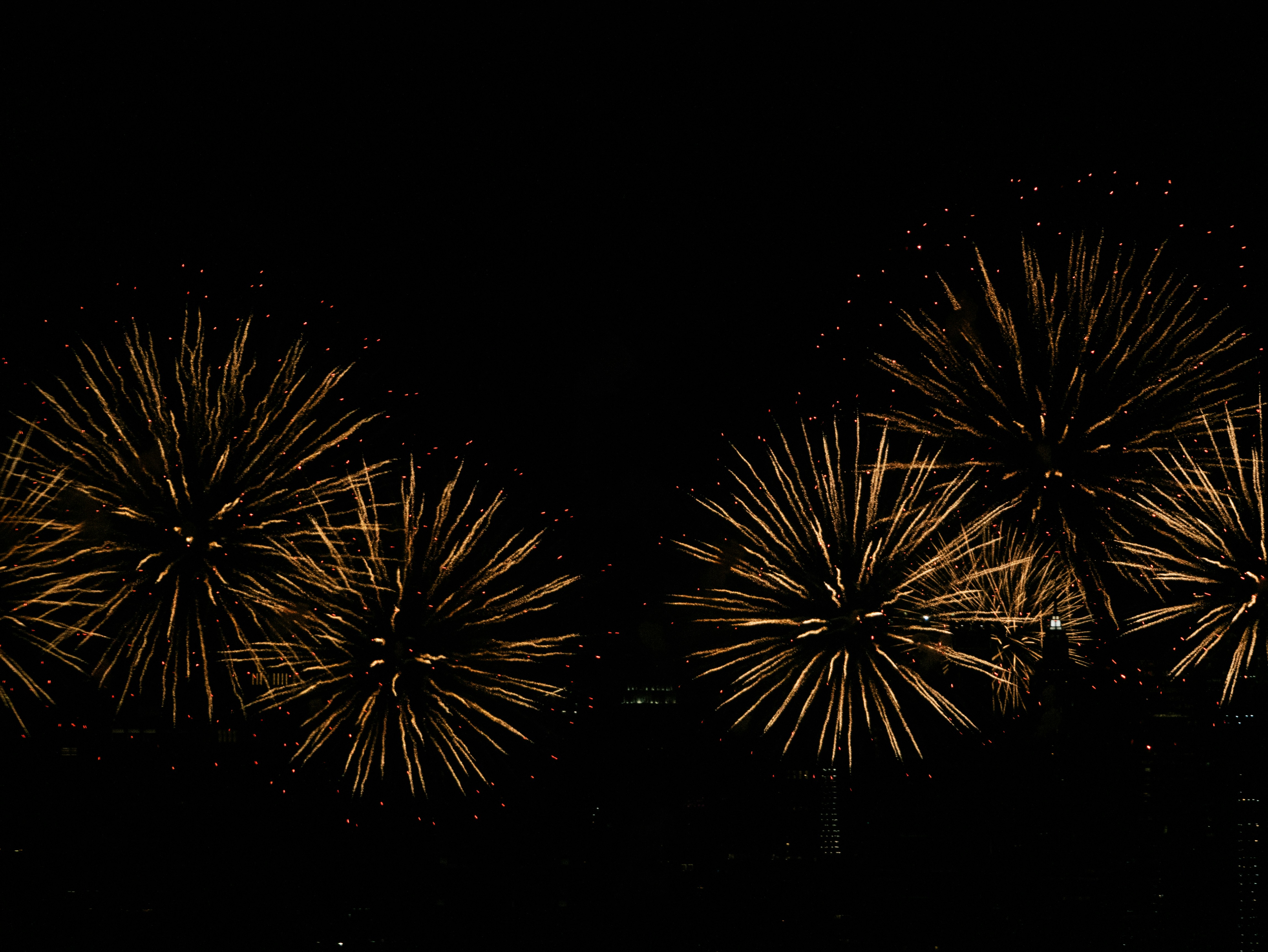 Golden fireworks bloom across a dark skyline, their radiating trails lighting the night. A celebration moment captured against a quiet city backdrop.