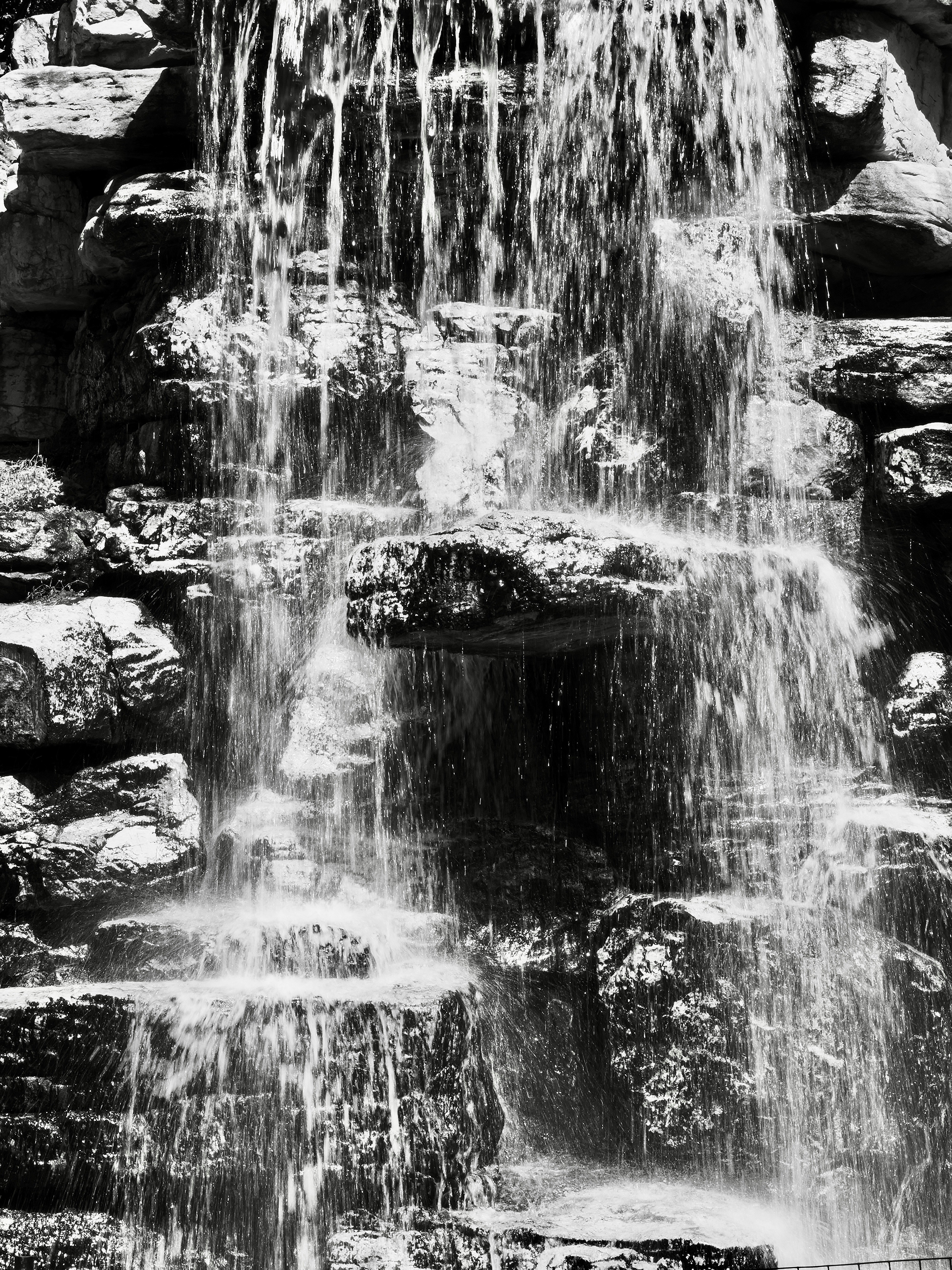 Monochrome waterfall spilling over rugged stone steps, emphasizing texture and motion in a rocky cascade. A sculpture-like composition with high-contrast details.
