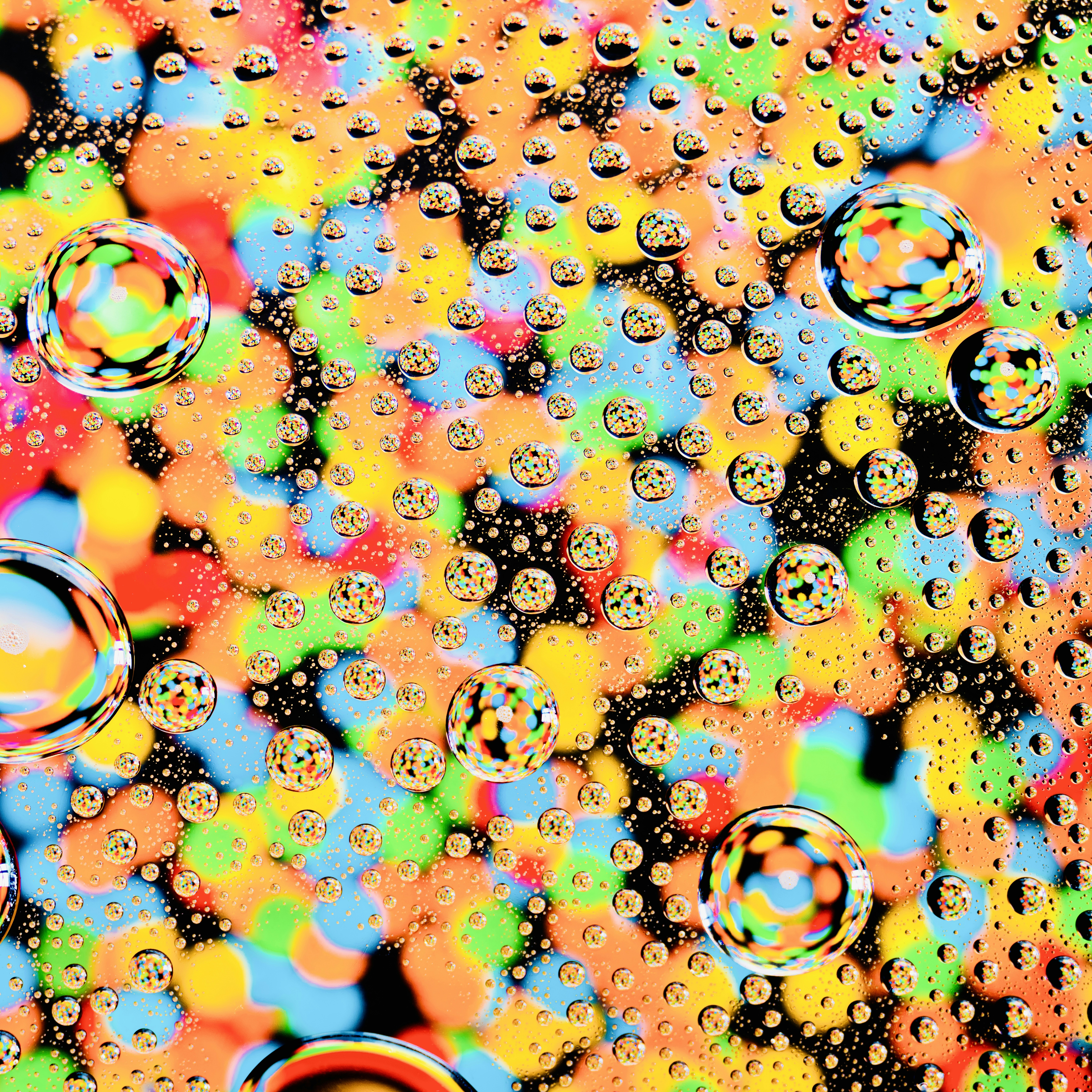A vibrant macro composition of multicolored beads and bubbles in clear liquid, creating a kaleidoscopic mosaic of hues and reflections. This is a close-up shot emphasizing texture and color, likely captured with macro lighting.