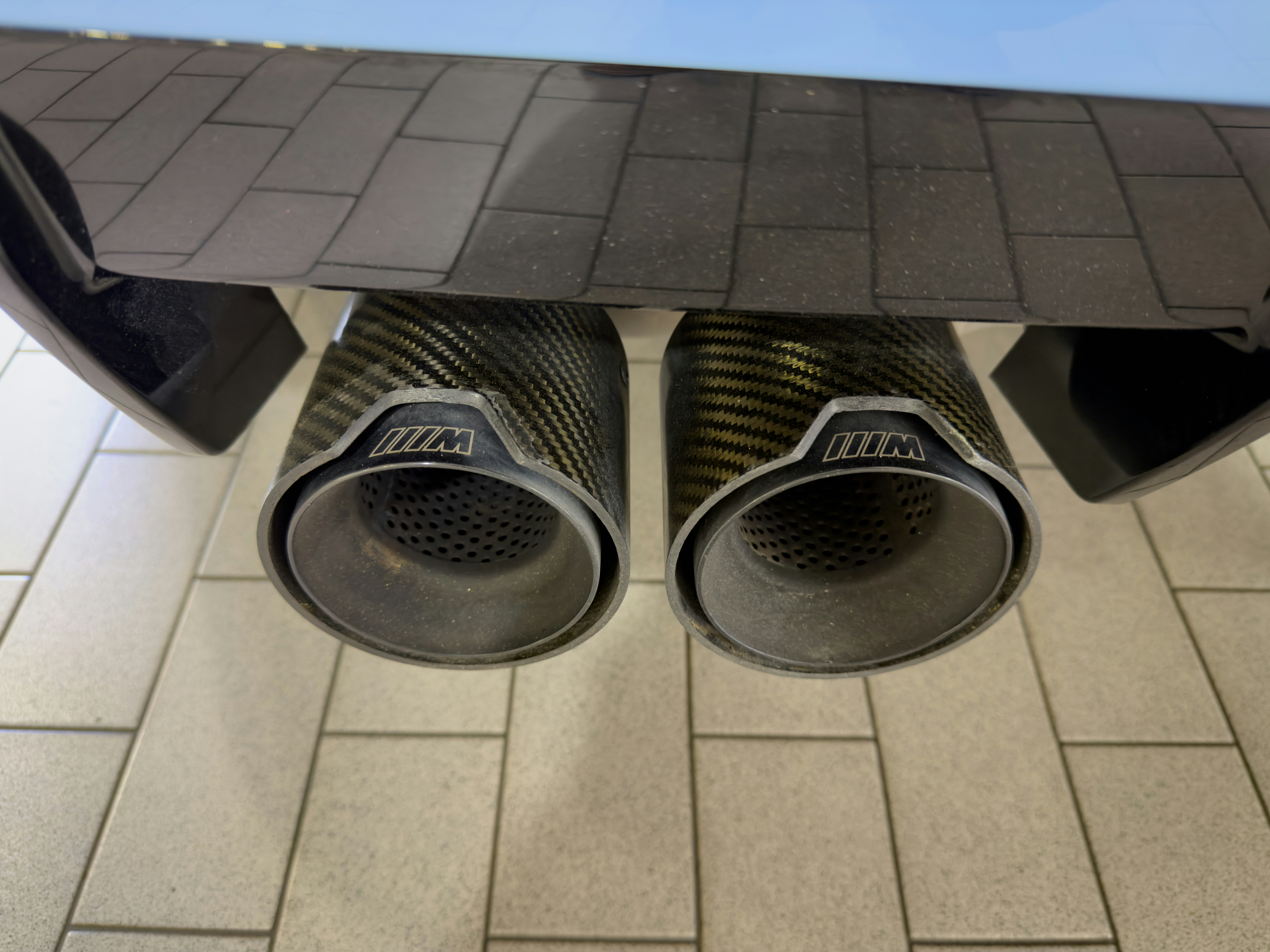 Dual exhausts in carbon weave undercarriage framed by showroom tiles