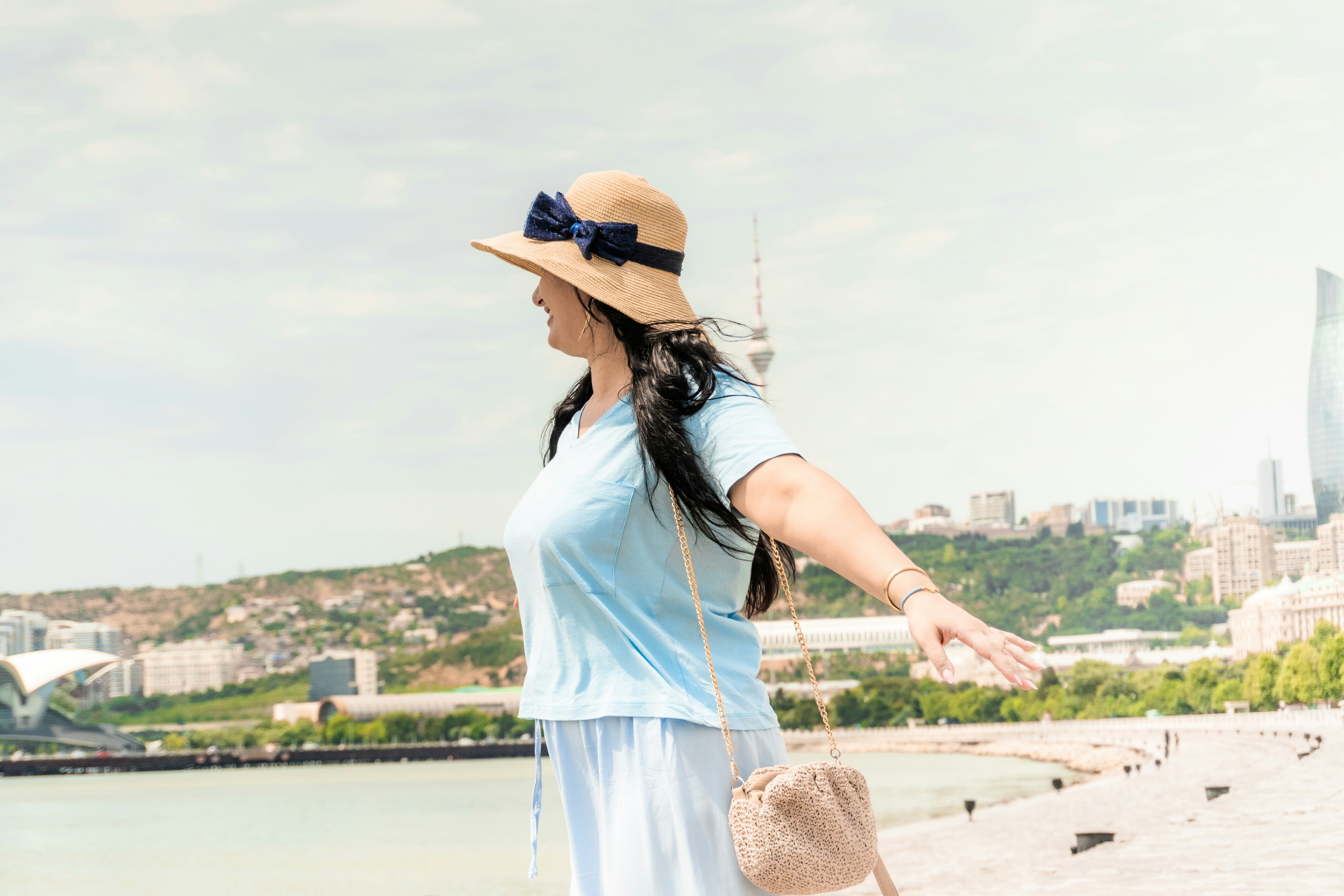 Sunlit Pose by the Seafront: A Woman in a Straw Hat Reaches Toward the Breeze