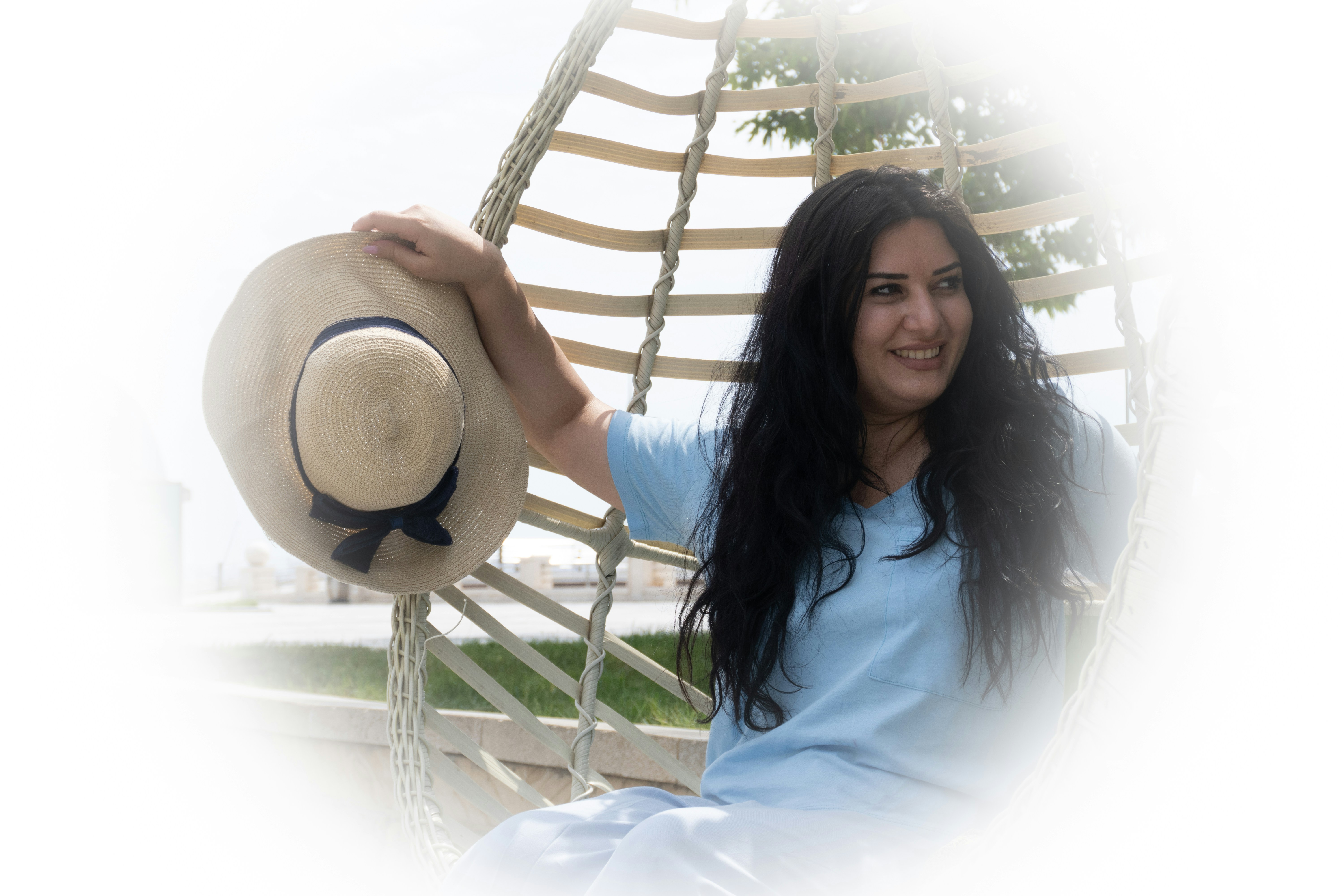 Sunlit portrait in a hanging chair with a straw hat