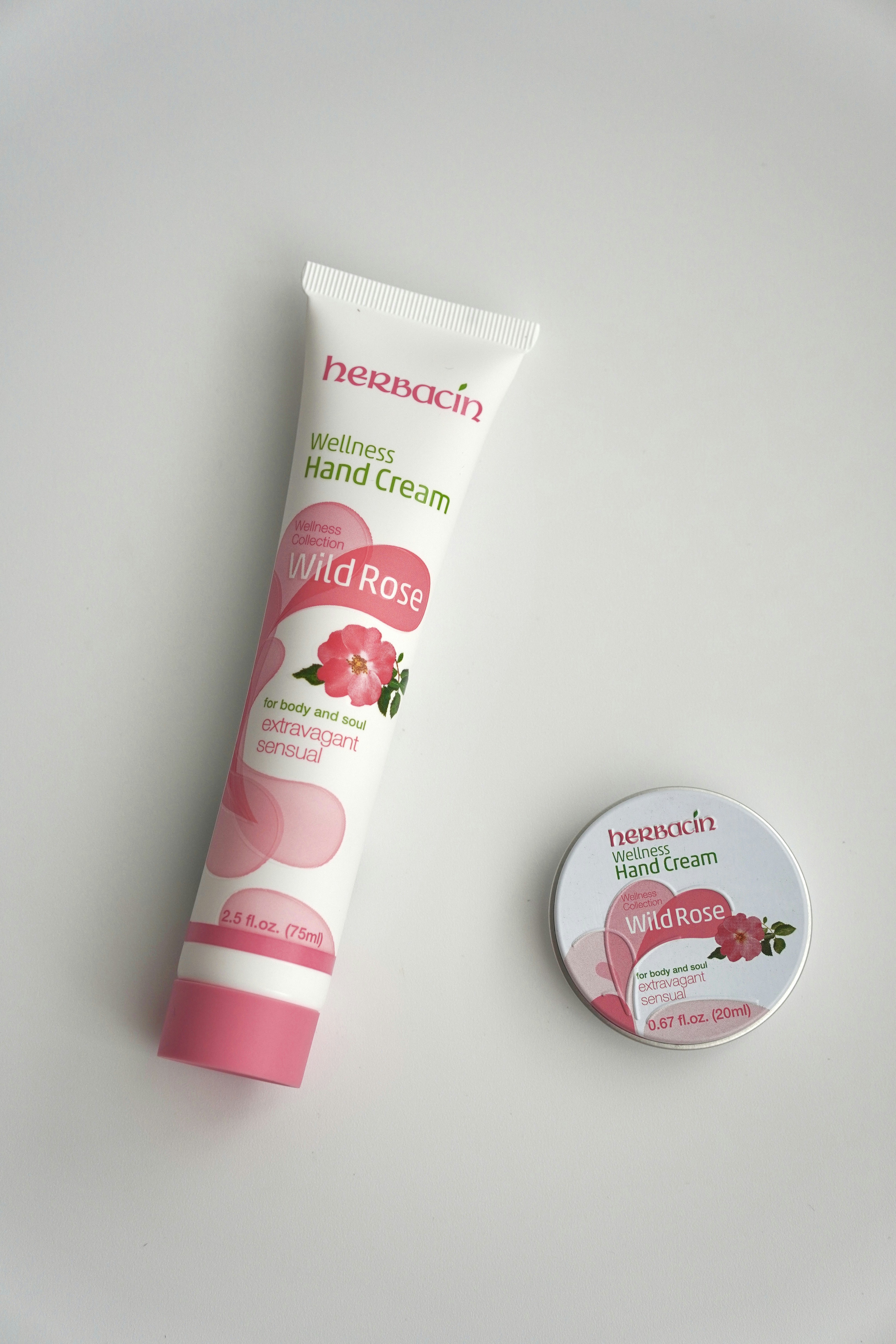 A white tube and small round tin of Herbalin hand cream labeled Wild Rose lie on a light surface, softly angled to showcase branding and floral design.