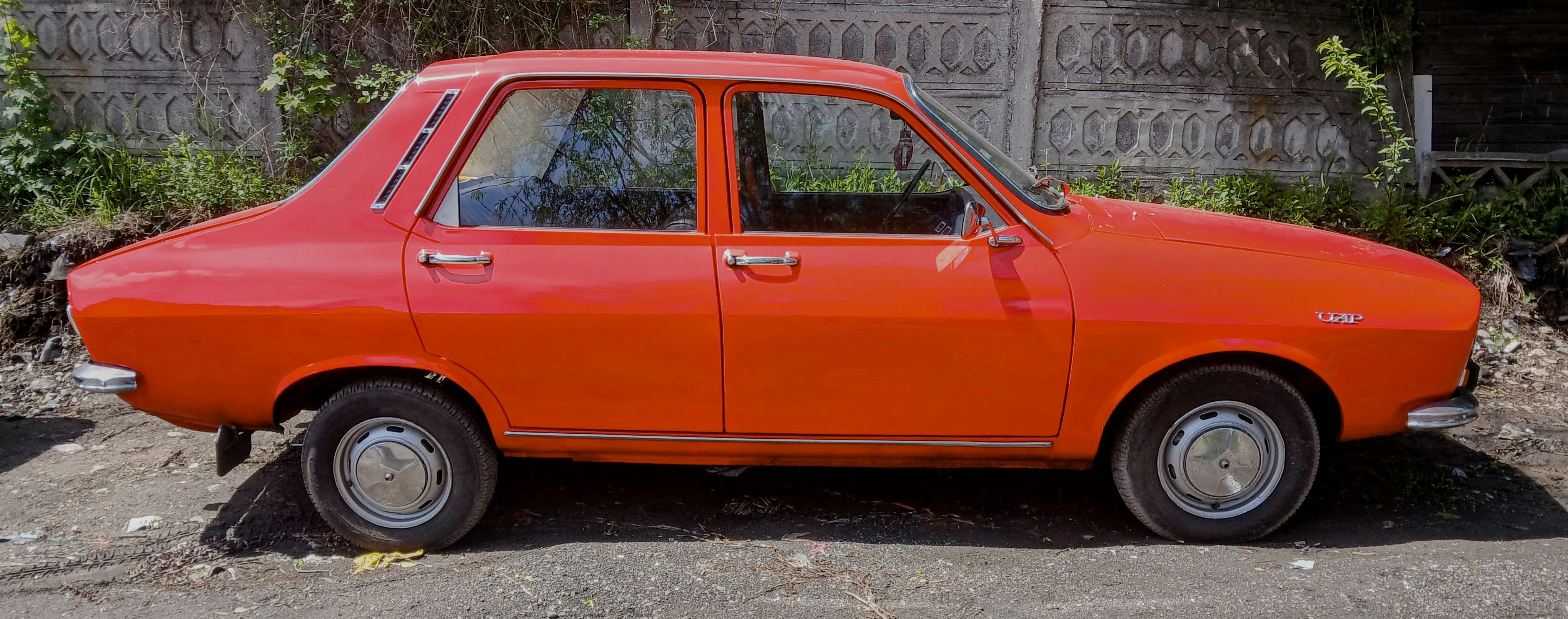 An orange vintage car parked by a fence.