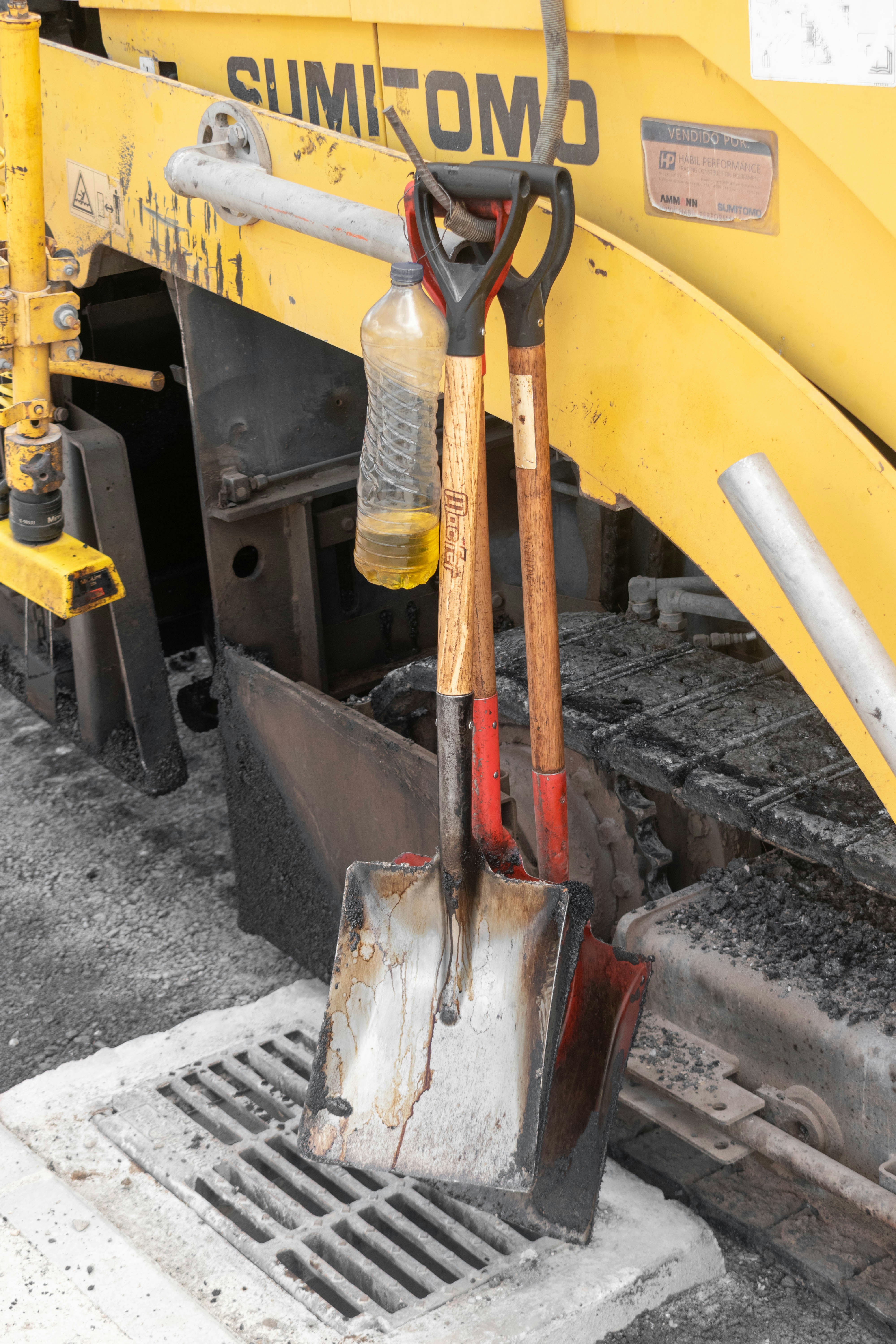 Shovel Standby: A Dusty Pair Leaning Against a Heavy-Lift in Yellow Machinery