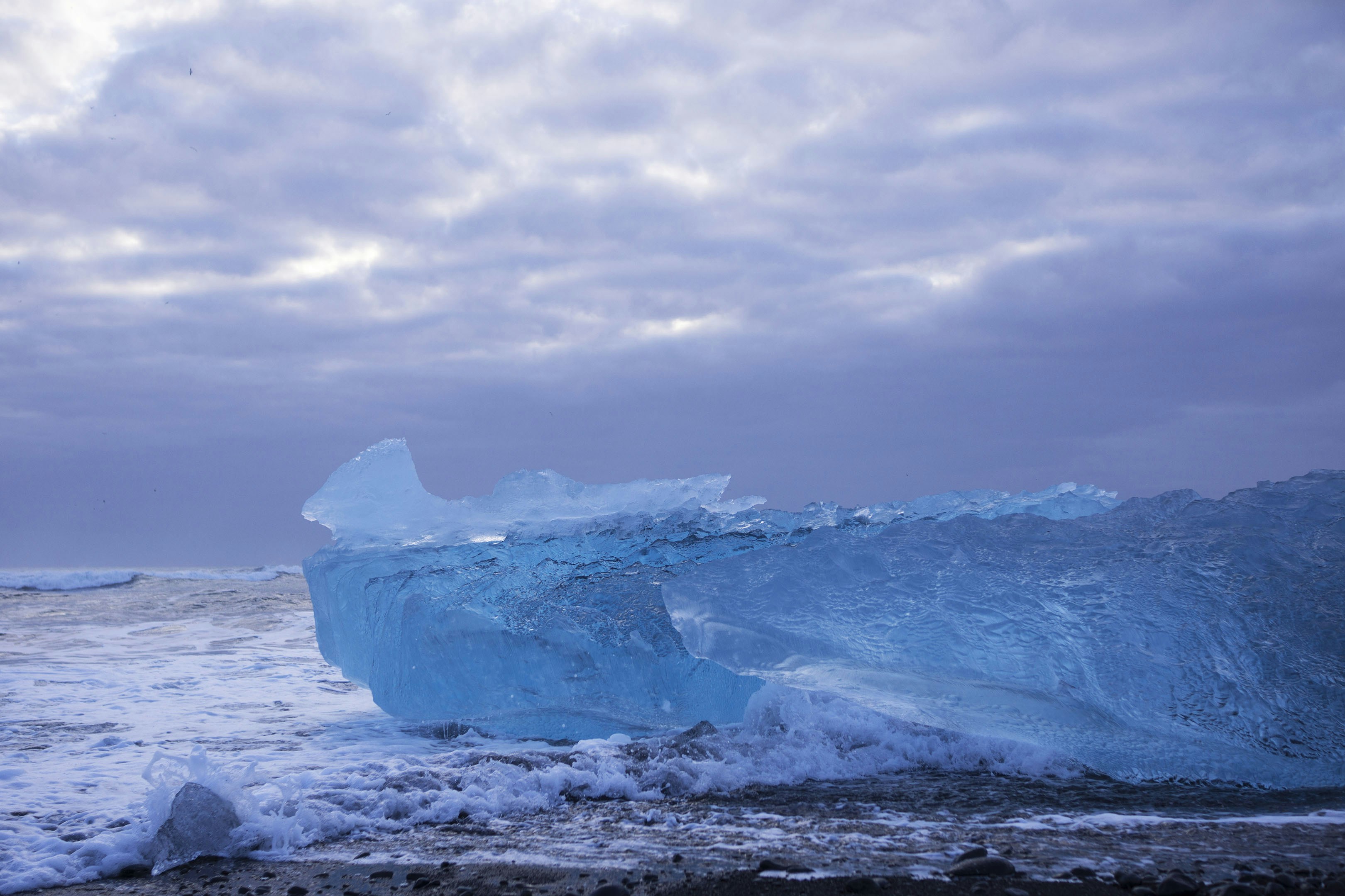 A lone blue iceberg resting on a stark icy shoreline under a moody sky