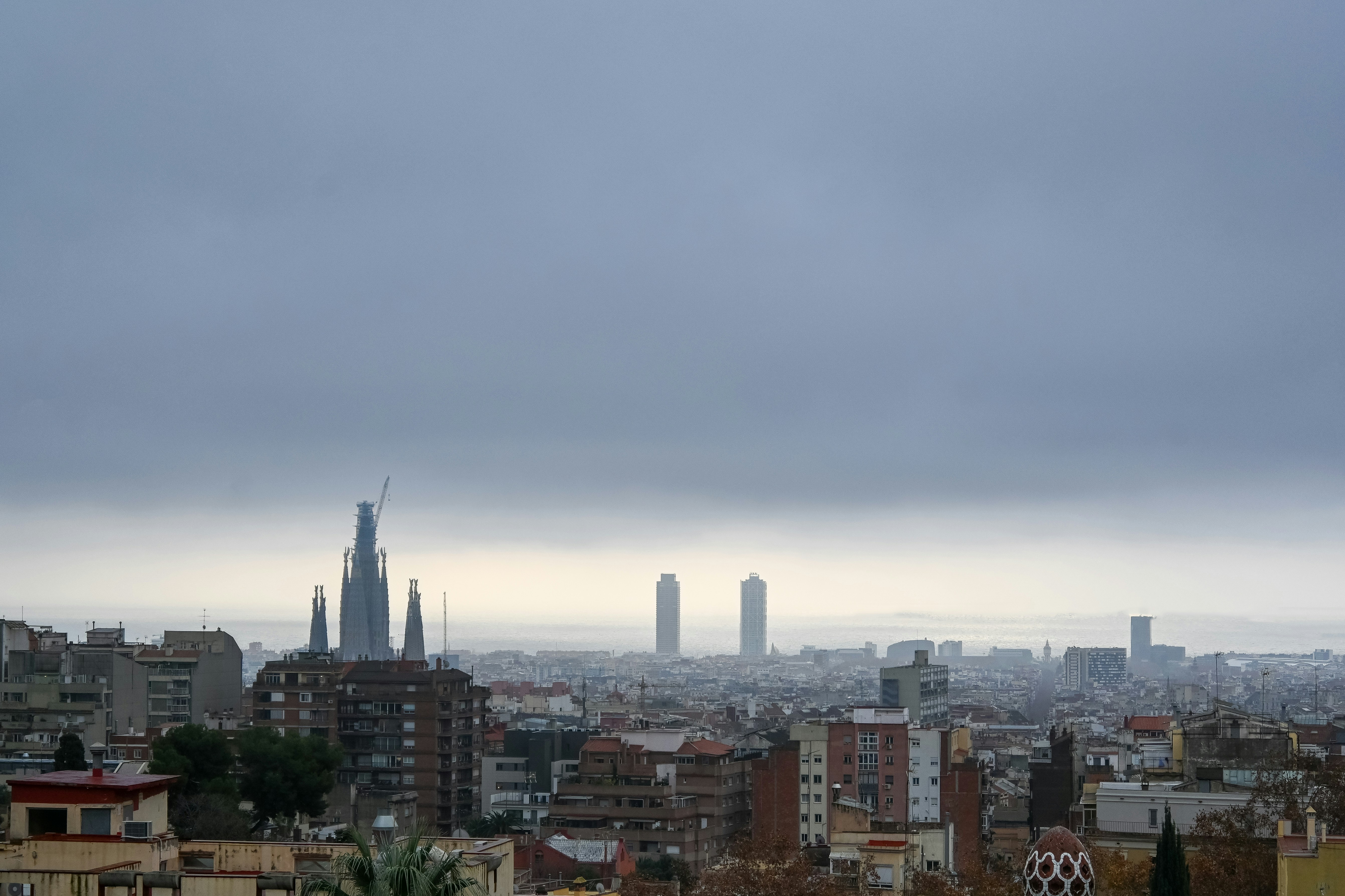 Urban horizon with distant high-rise silhouettes under a moody, overcast sky; foreground shows a dense mid-rise neighborhood. A quiet cityscape emphasizing atmosphere and depth.