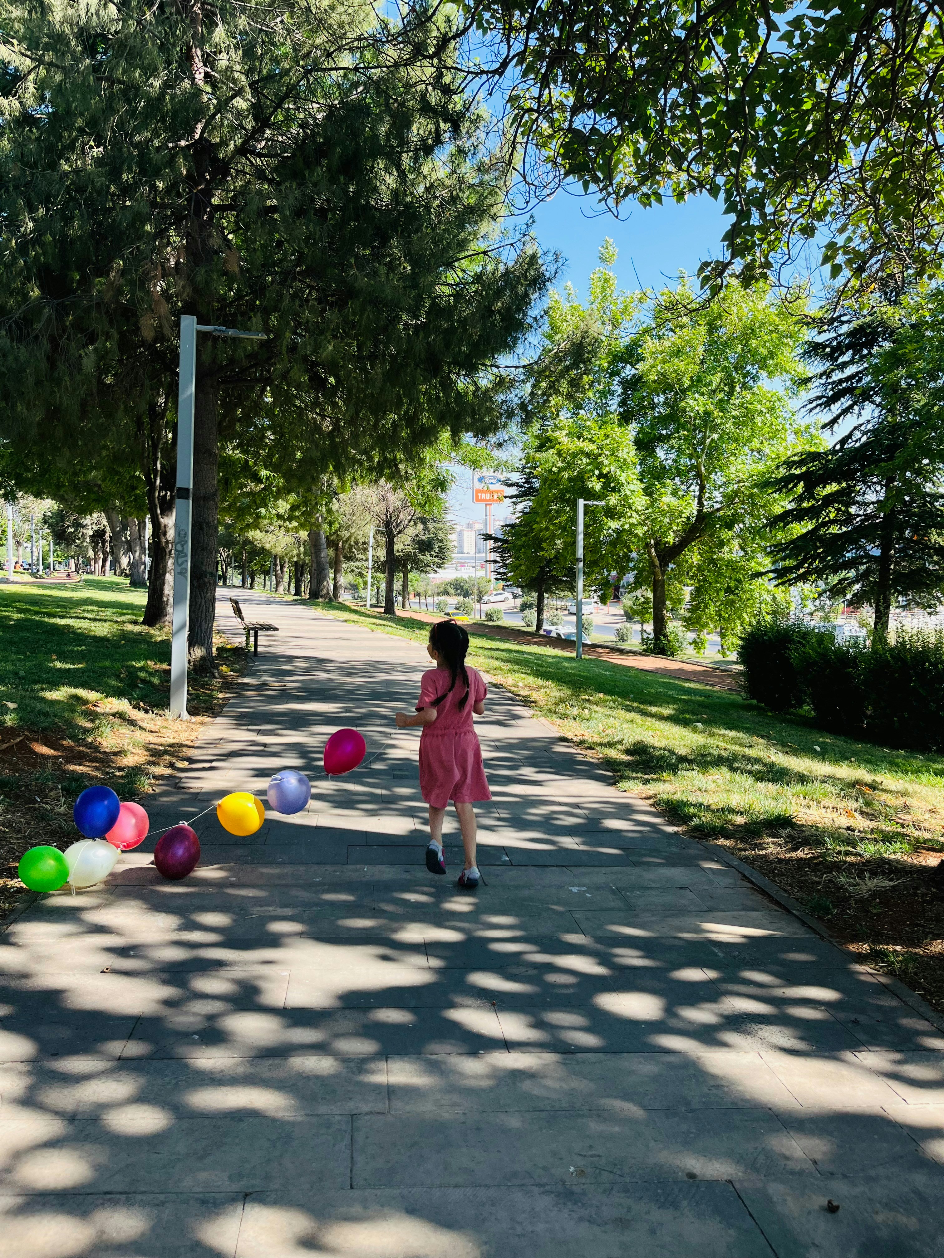 Girl Chasing Colorful Balloons on a Shaded Park Path