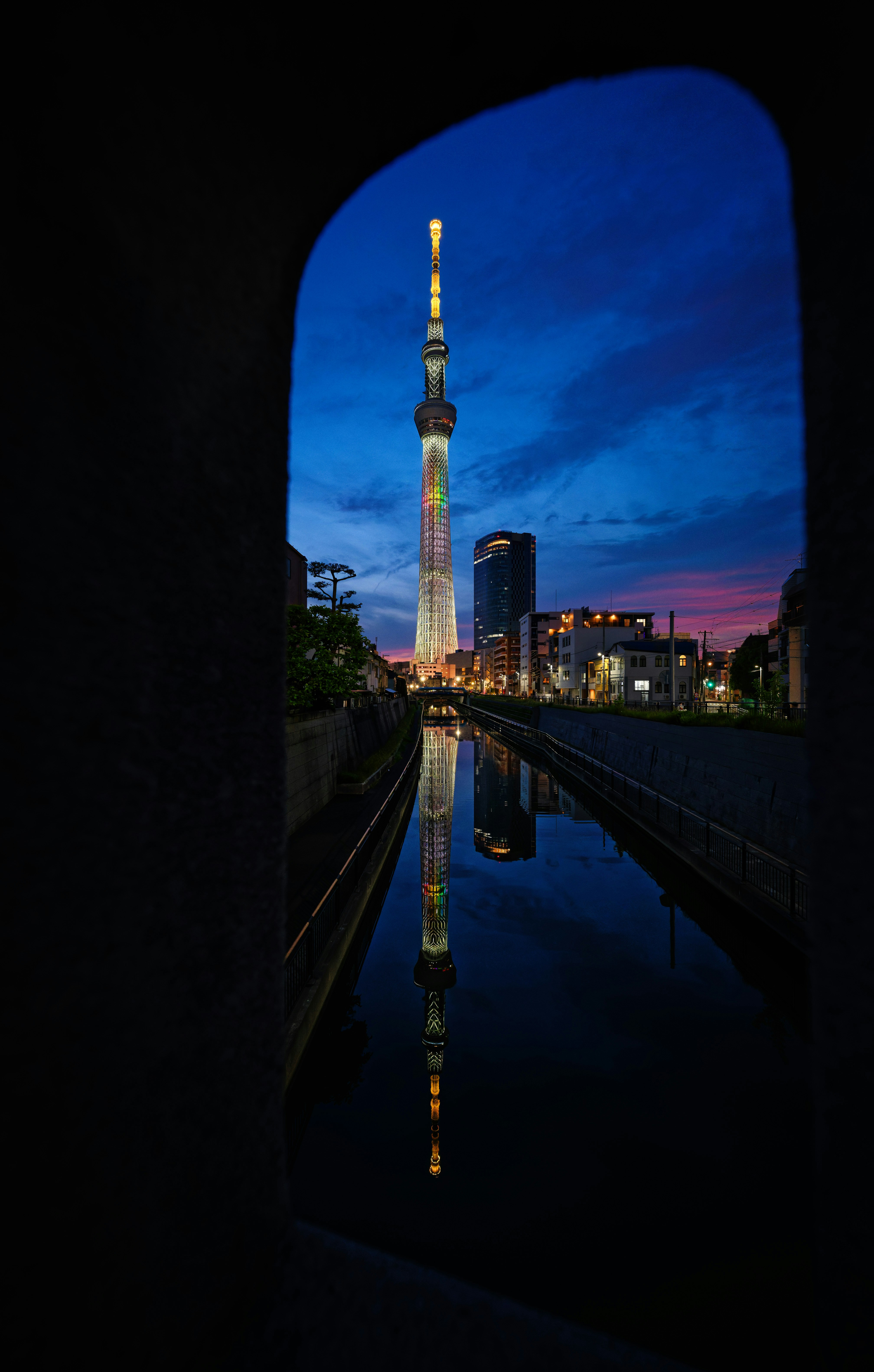 Illuminated tower reflects in canal at twilight, framed view.