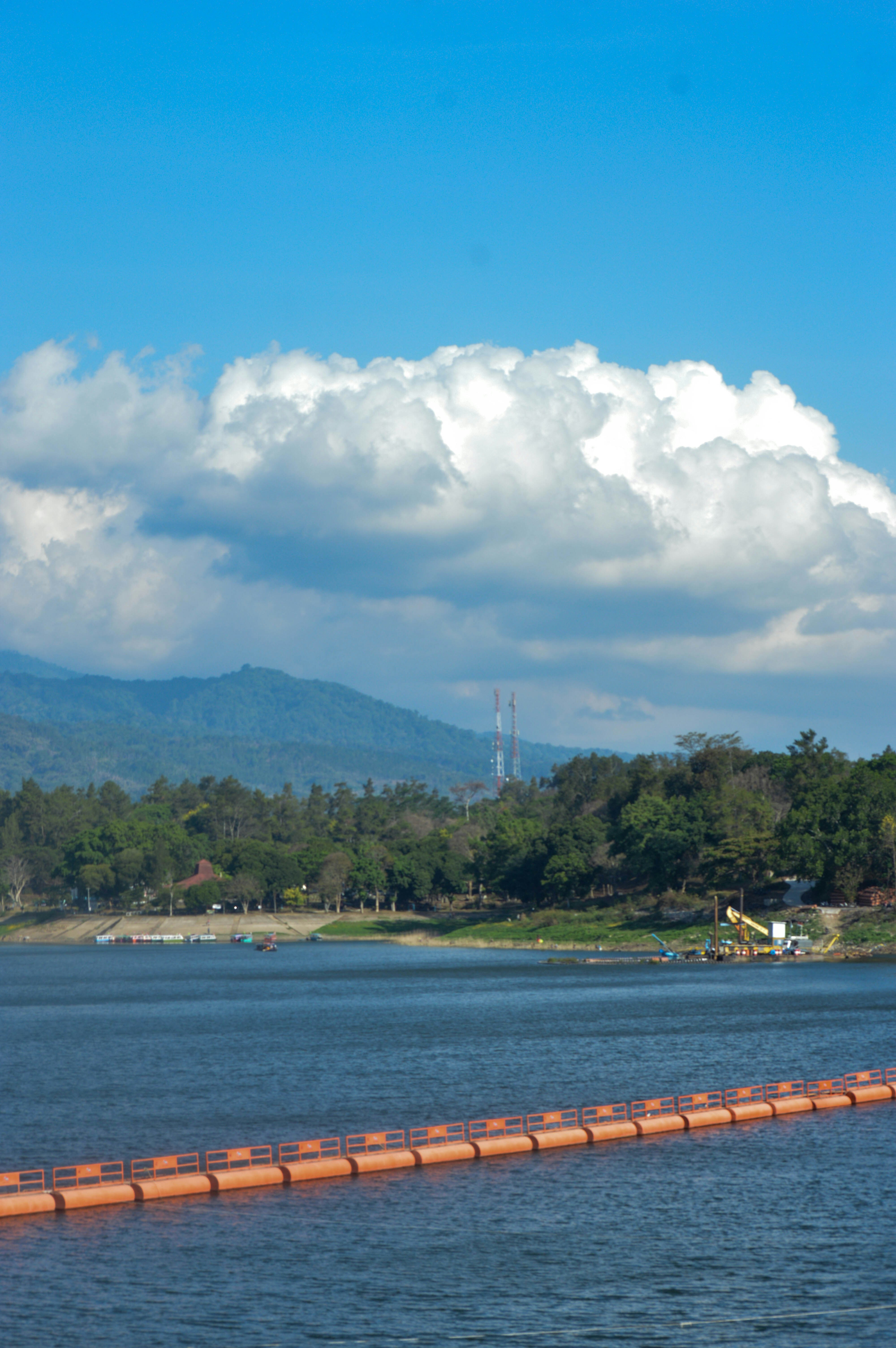 Serene lakeside contrast: distant hills, drifting cloudscape, and a buoyant barrier