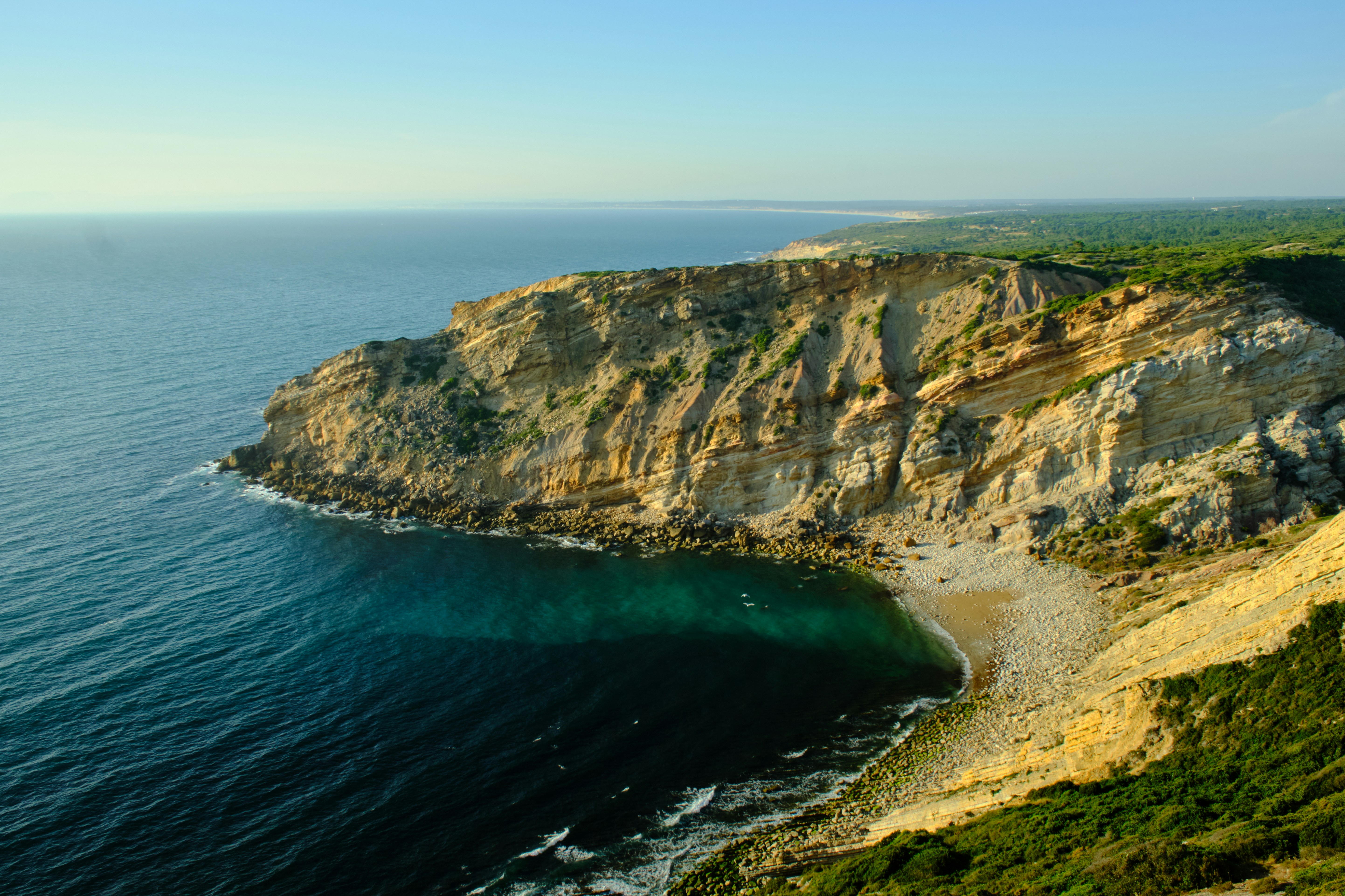 Dramatic cliffs overlooking a serene ocean with a secluded beach.