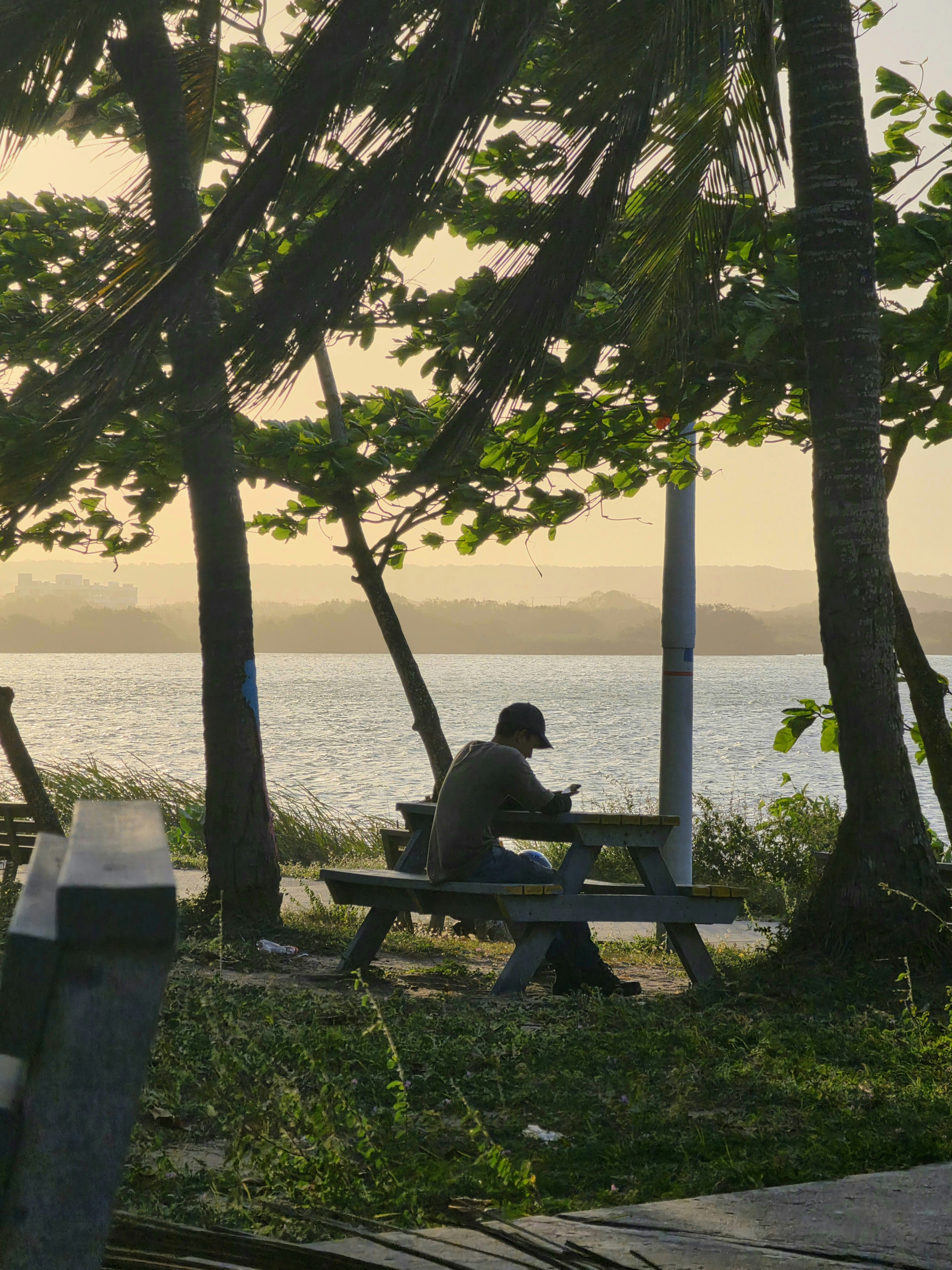 Man on a picnic bench by the water at sunset.