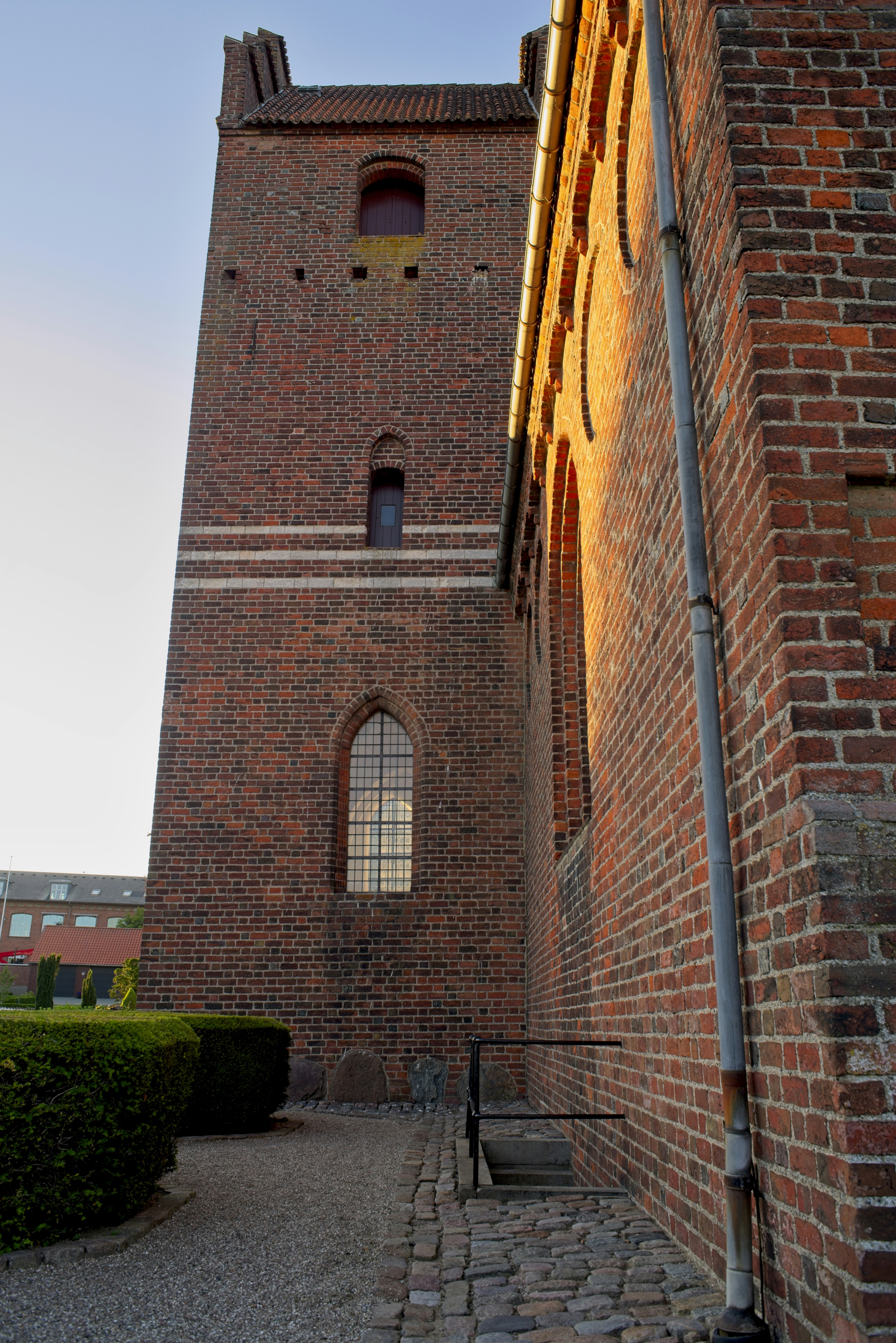 Brick Tower at Dusk: Narrow Path, Warm Facade, and Arched Window