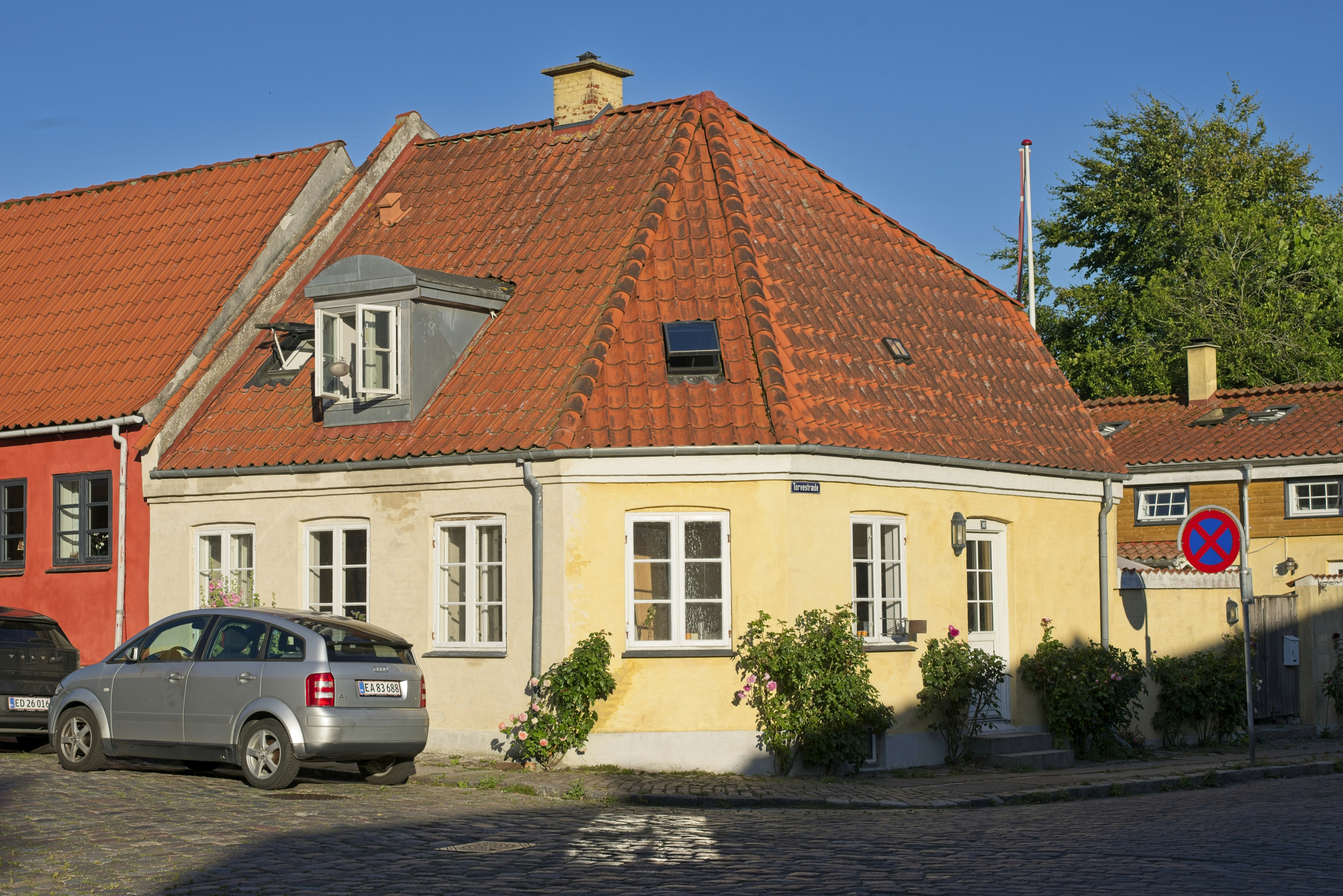 Sunlit Corner House with Red Tiled Roof on Quiet Cobblestones