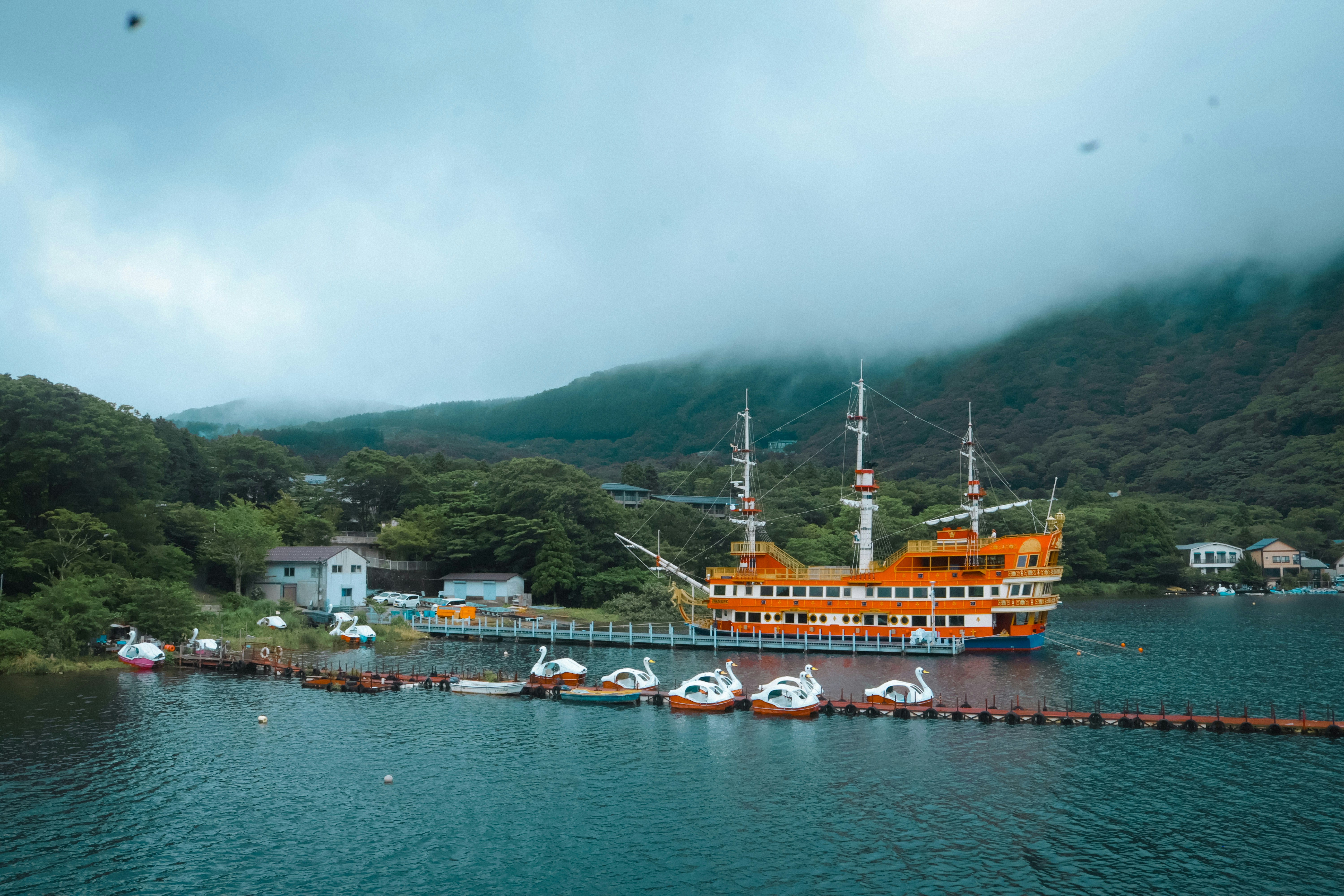 Orange sailing ship anchored in a tranquil lakeside harbor
