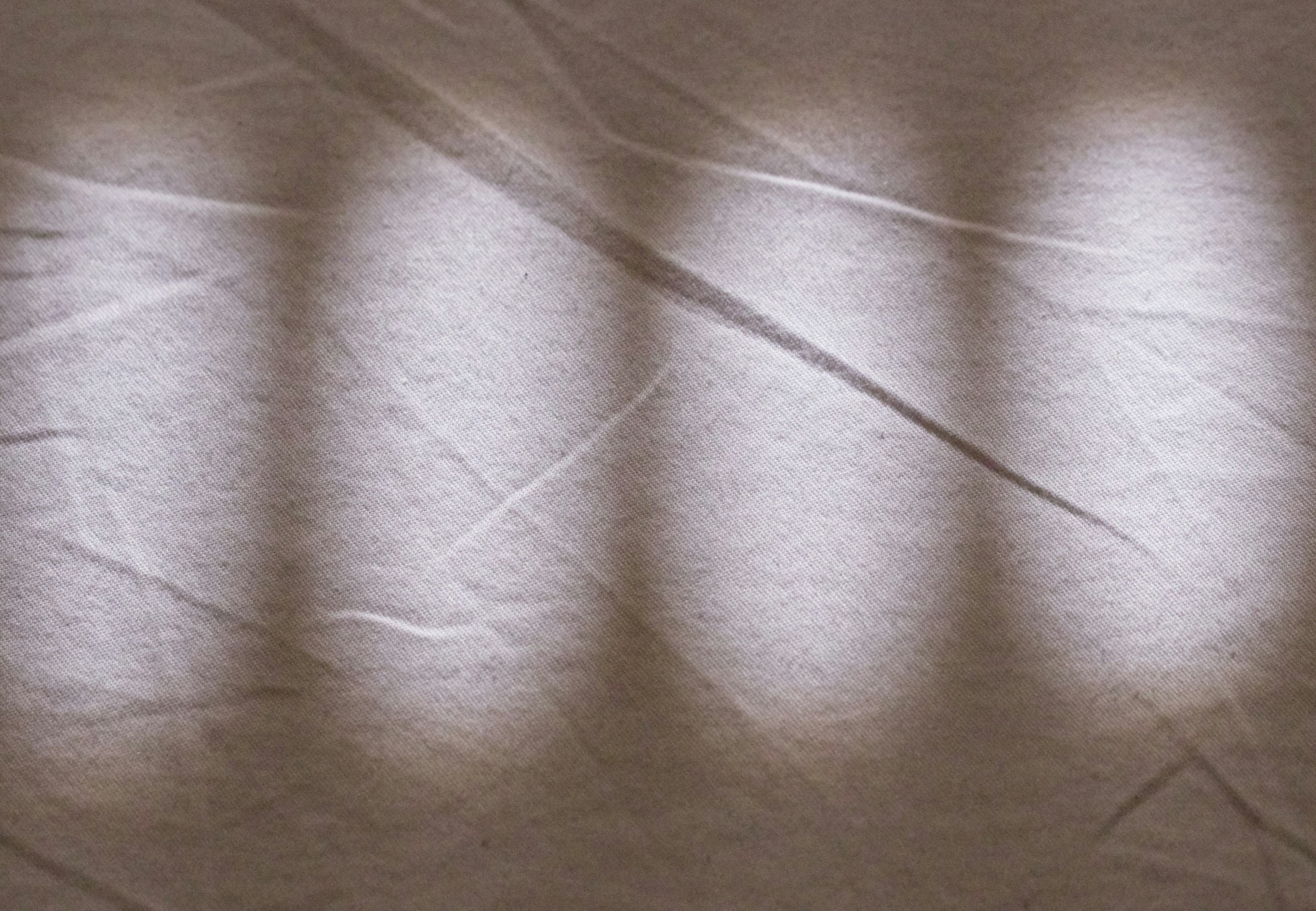 Abstract texture with soft folds and subtle creases on a beige surface, resembling crumpled paper or fabric with gentle tonal shifts. A minimal, artistic close-up that emphasizes material and light.