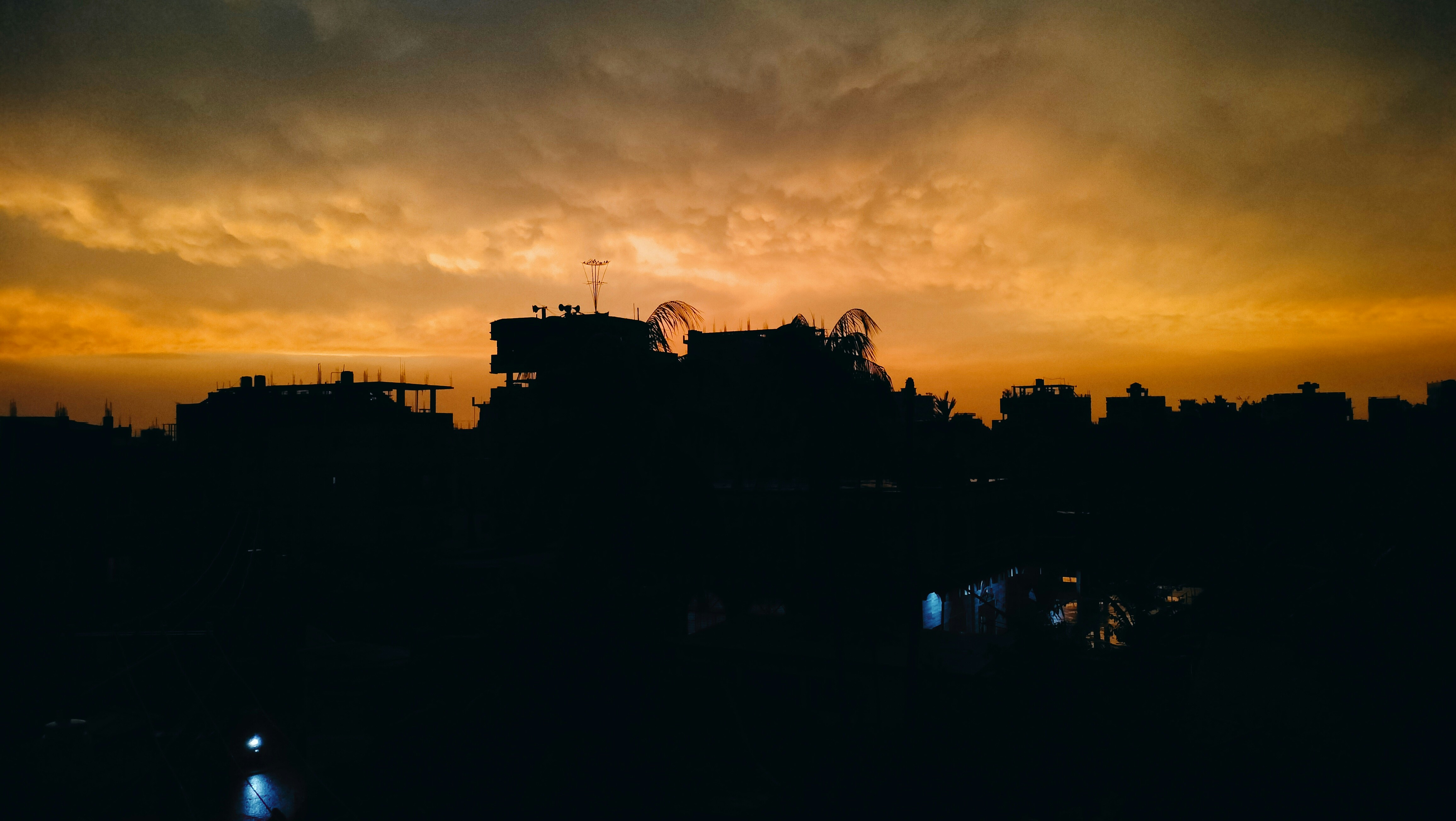 Dusk sky glows orange behind a dark city skyline, leaving the buildings as a crisp silhouette against the fiery horizon.