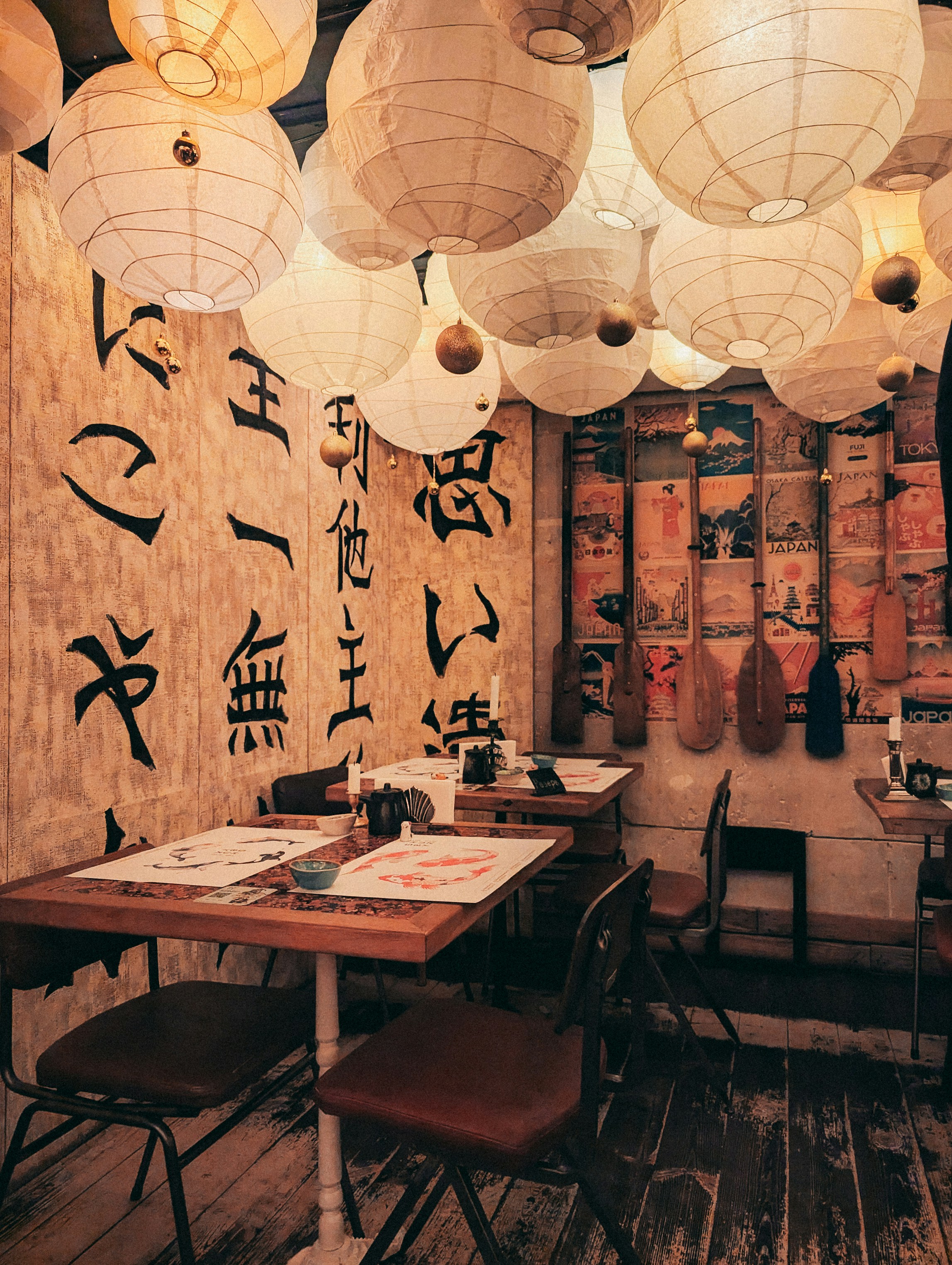 Warm-toned interior of a cozy restaurant with hanging paper lanterns, wooden tables, and Japanese calligraphy on the wall, creating an ambient dining scene.