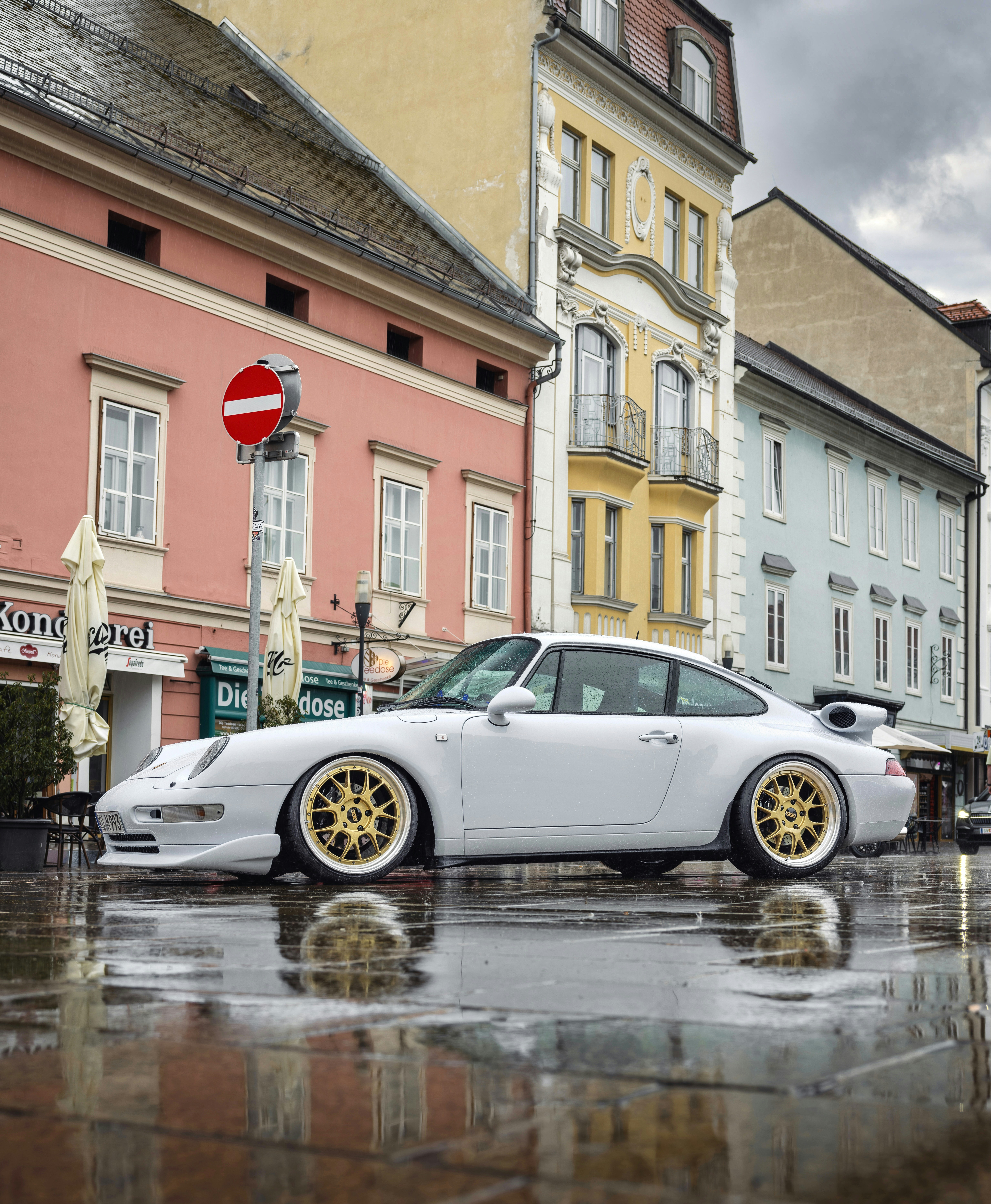 White Porsche Stretches its Shadow Across a Rainy European Street