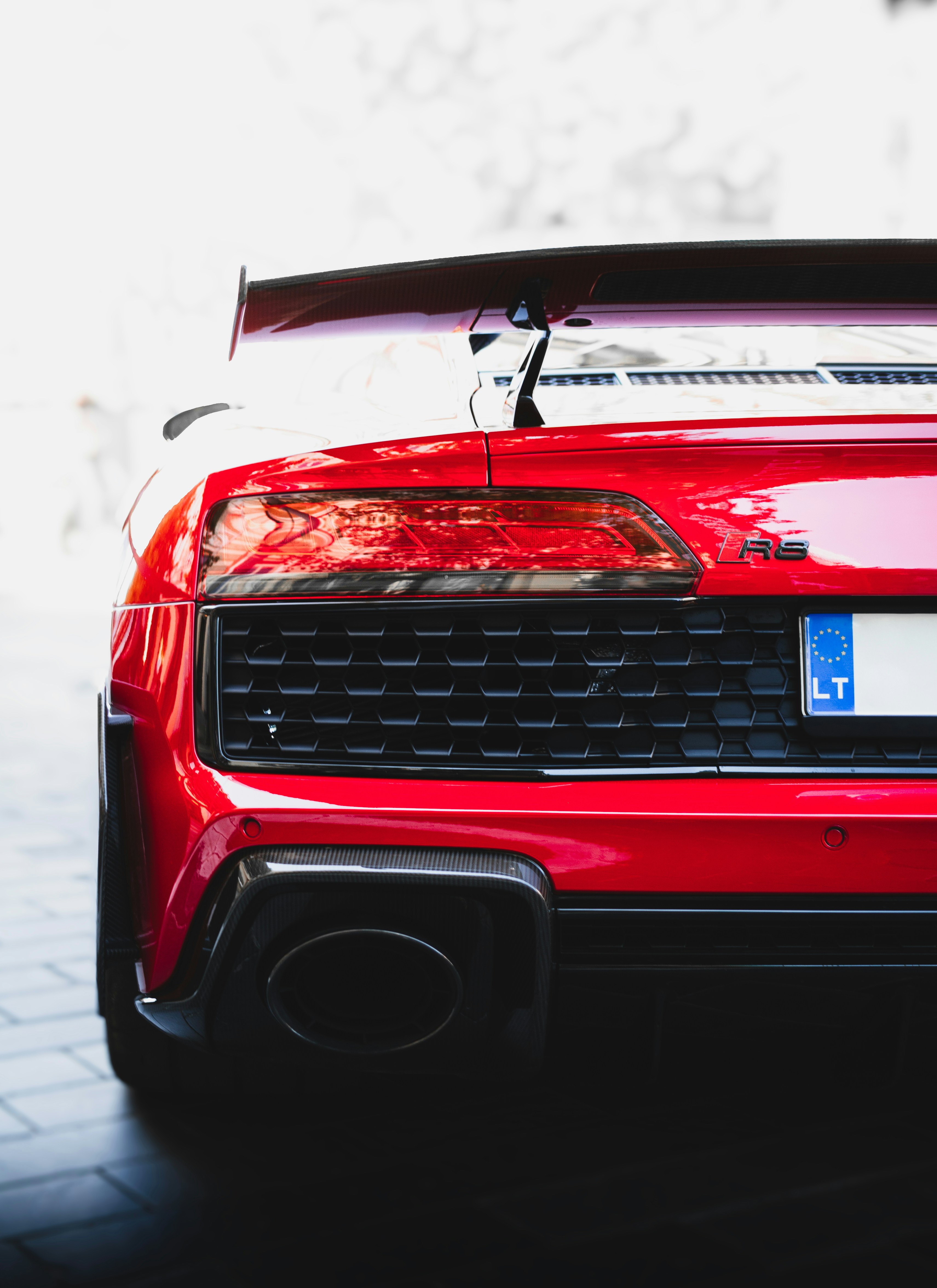 Close-up of the rear end of a red sports car, highlighting the taillights, honeycomb grille, and exhaust; the scene emphasizes the vehicle's design and glossy finish.