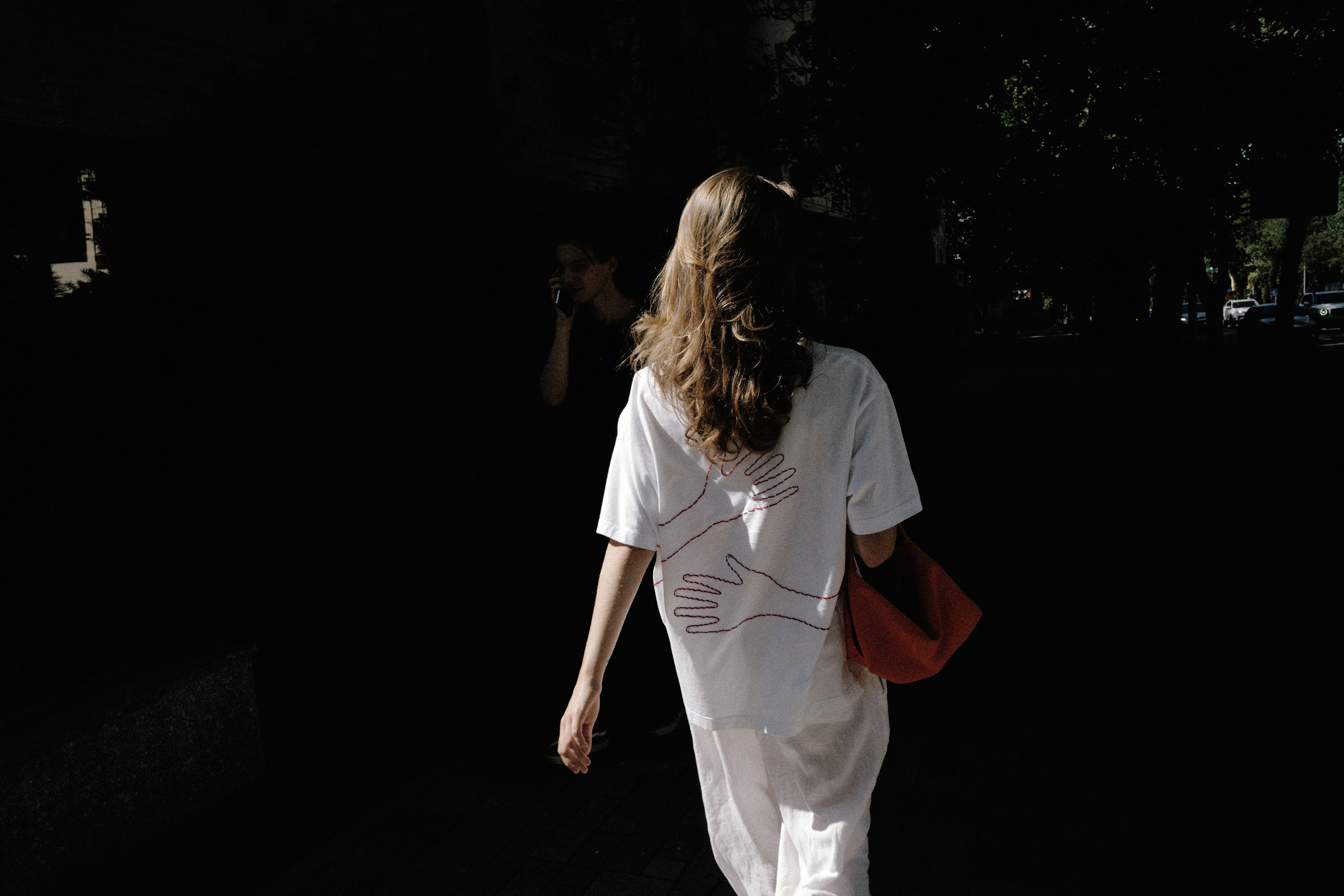 Backlit Walk: A White Garment and a Red Accent Amid Shadowed Path