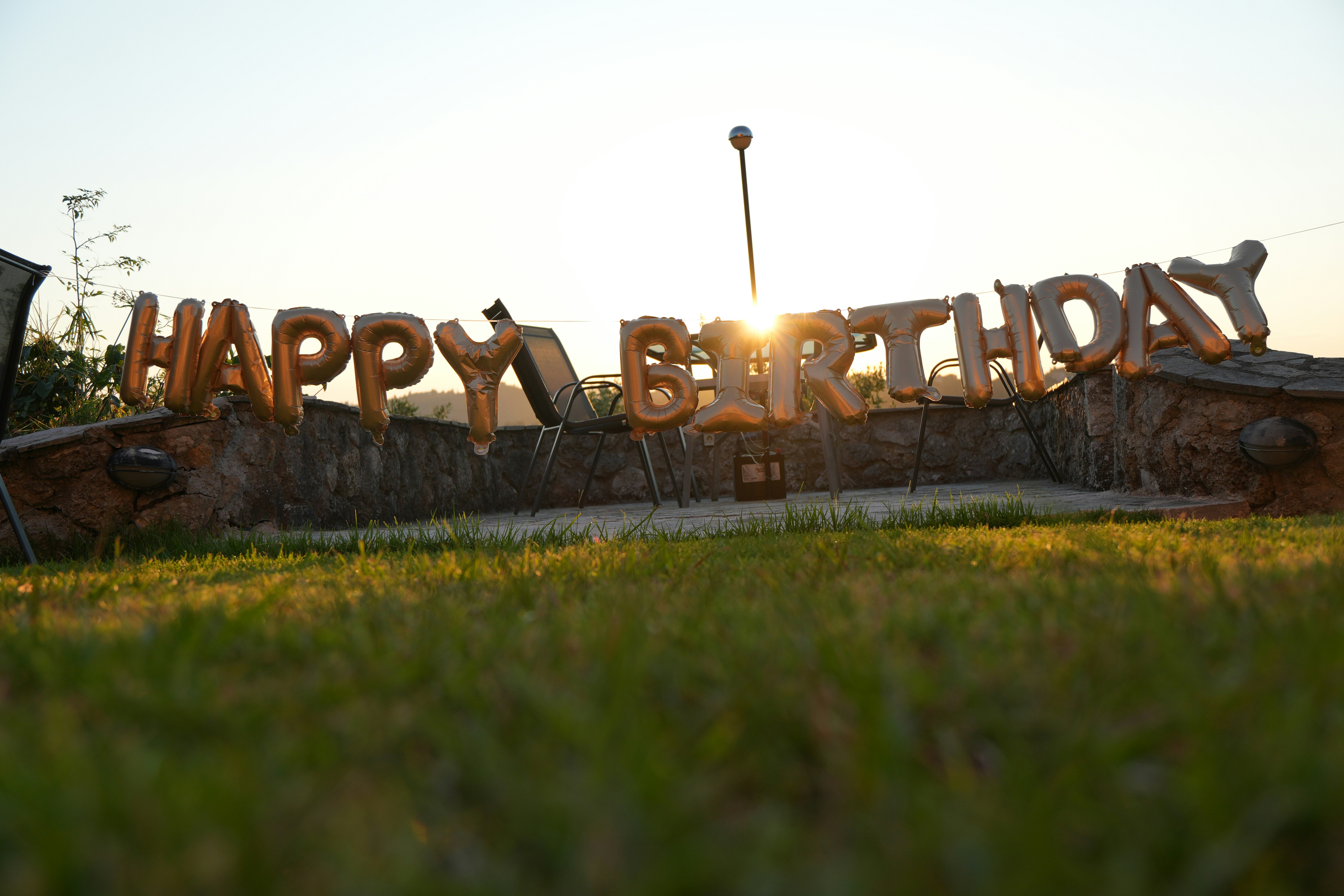 Birthday cheers in warm backlight: balloon letters rise over a rustic mural