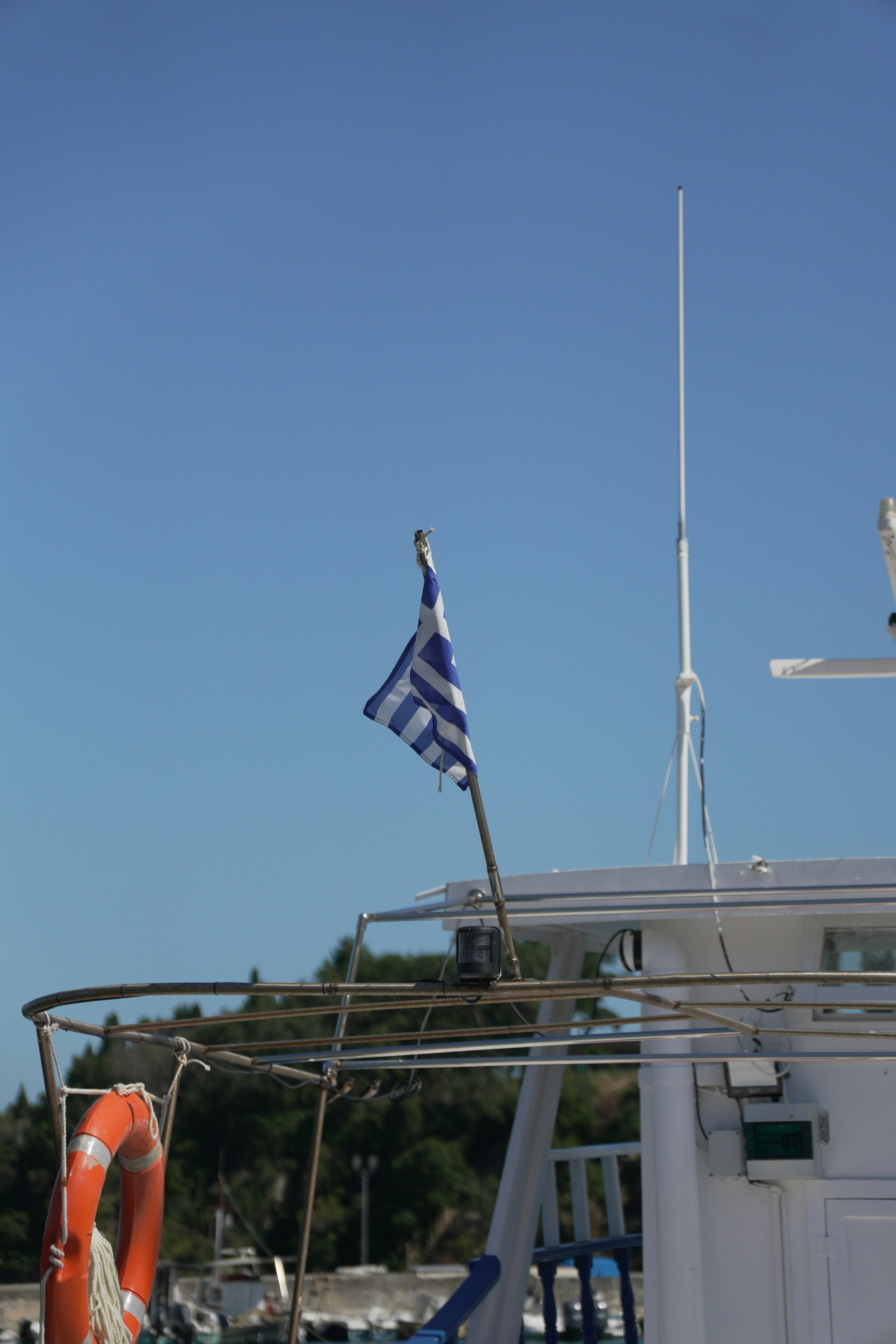 Flag at the Bow: Greek Flag Flank Above a Quiet Marina