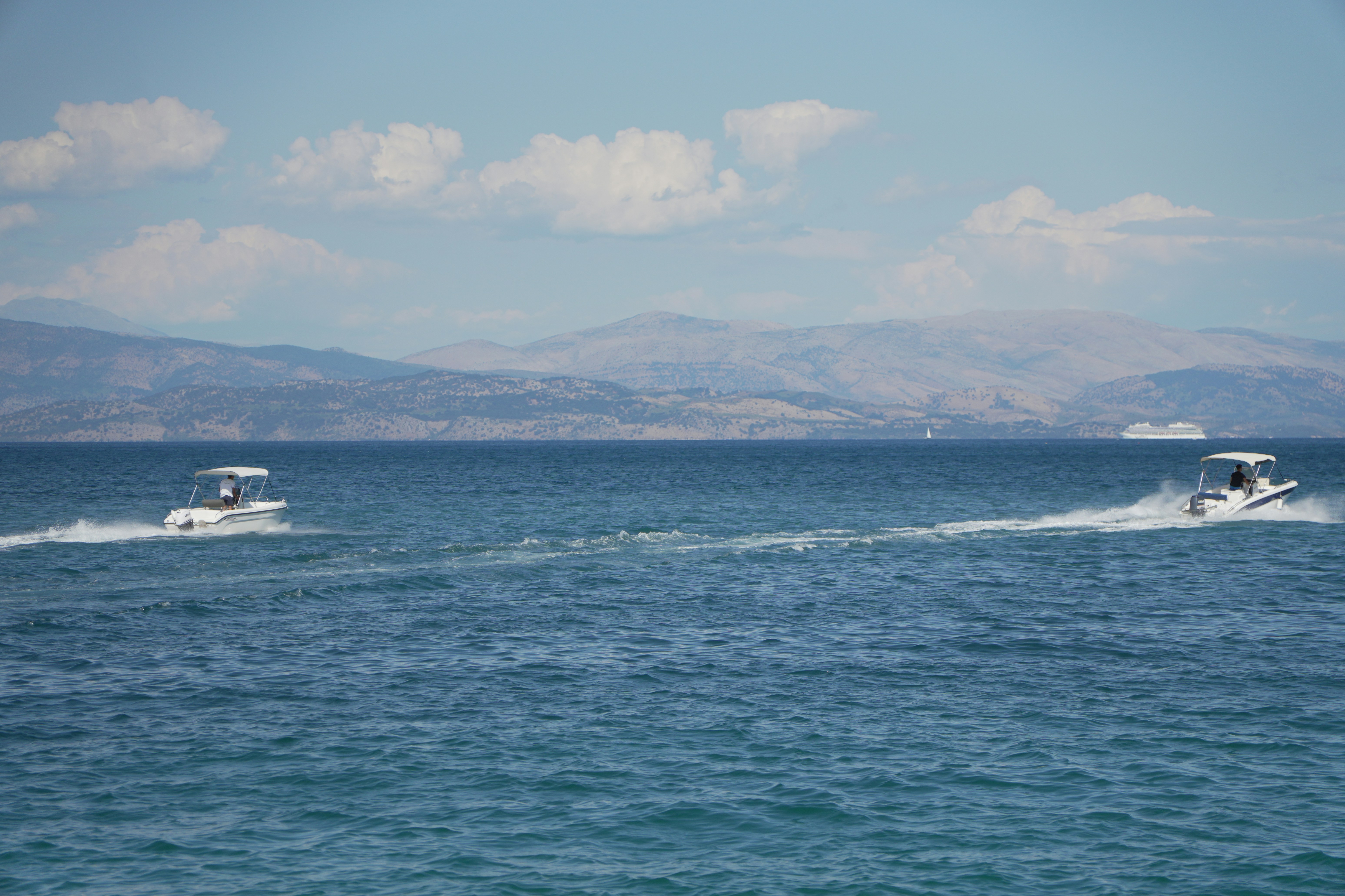 Twin wake: boats streaking across a calm blue sea toward distant mountains