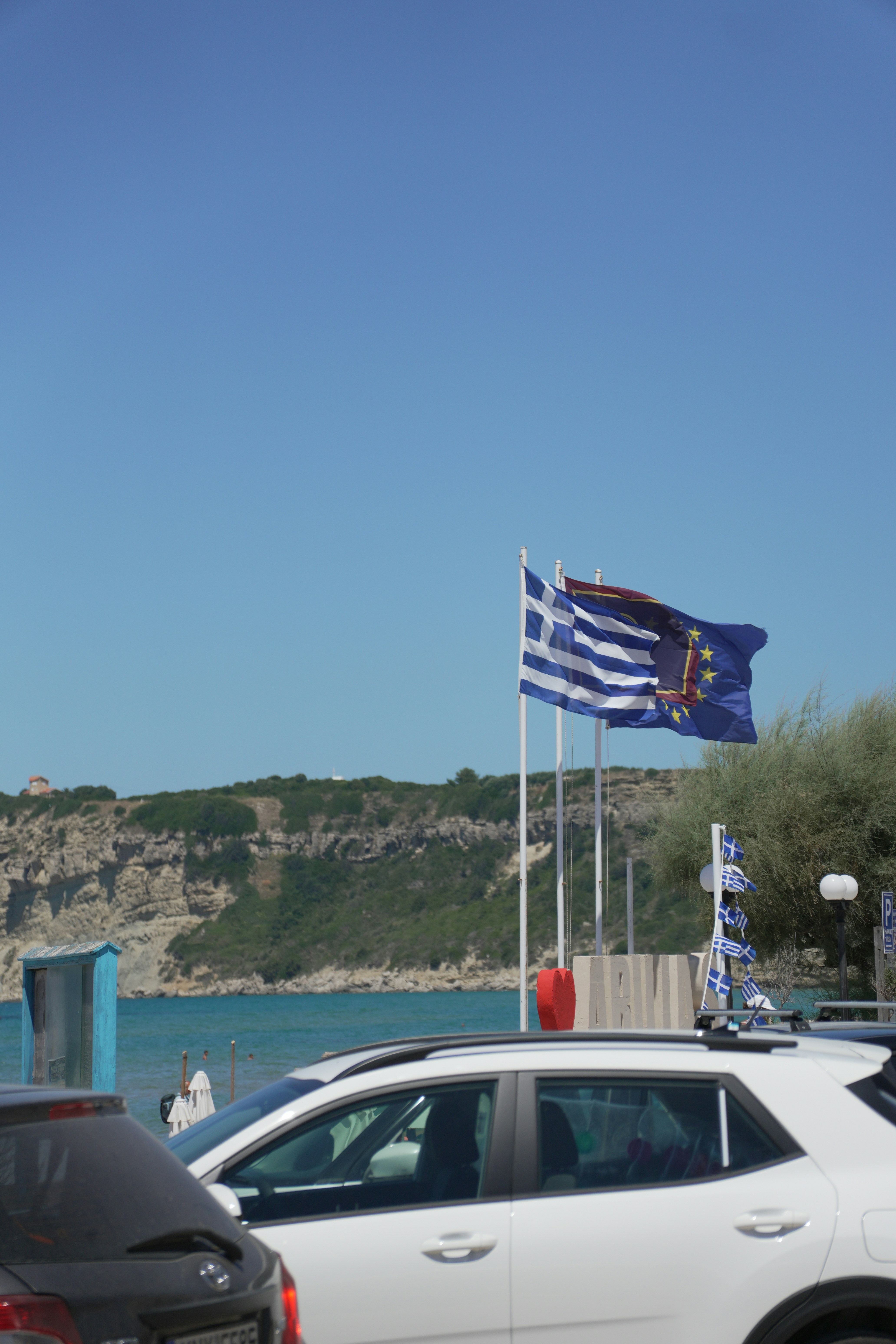 Flags Rise Over Coastal Scene with Parked Cars