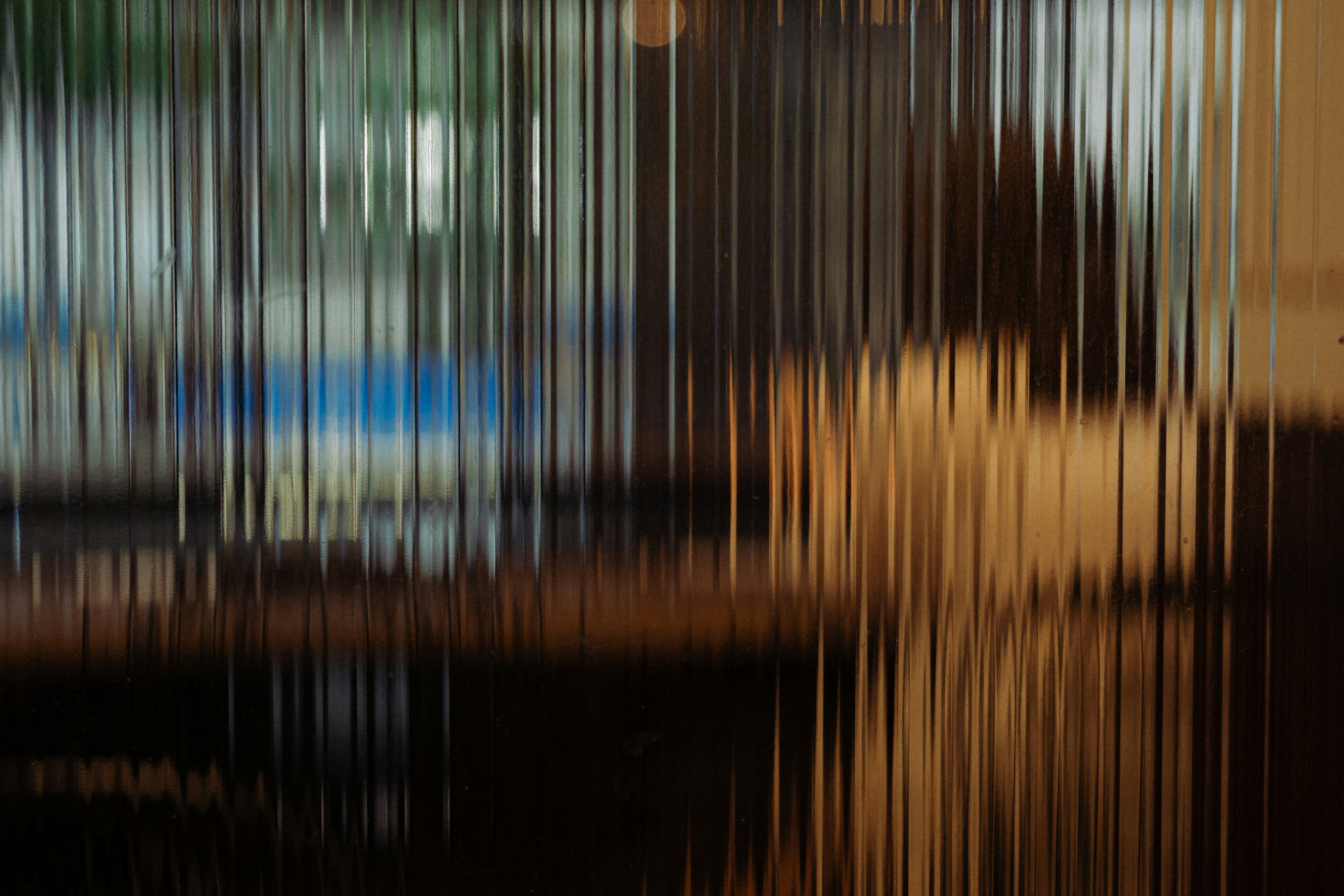 Abstract portrait captured through a warped glass surface with vertical distortions; hints of a figure blurred into warm amber tones and dark foreground. This is a photographic study, not a logo or illustration.