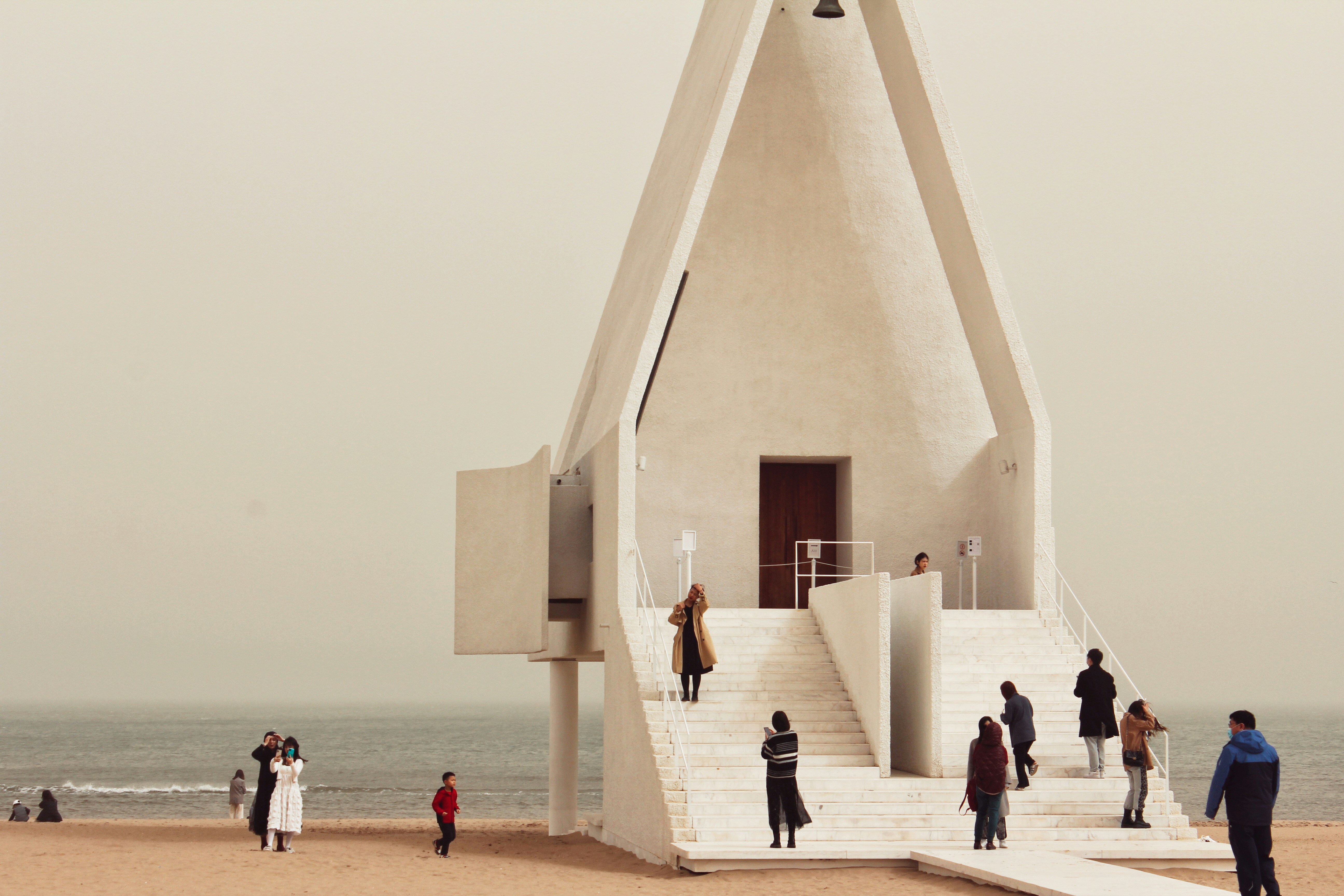 Seaside Chapel Ascent: Visitors Gather at a White Concrete Monument by an Empty Horizon