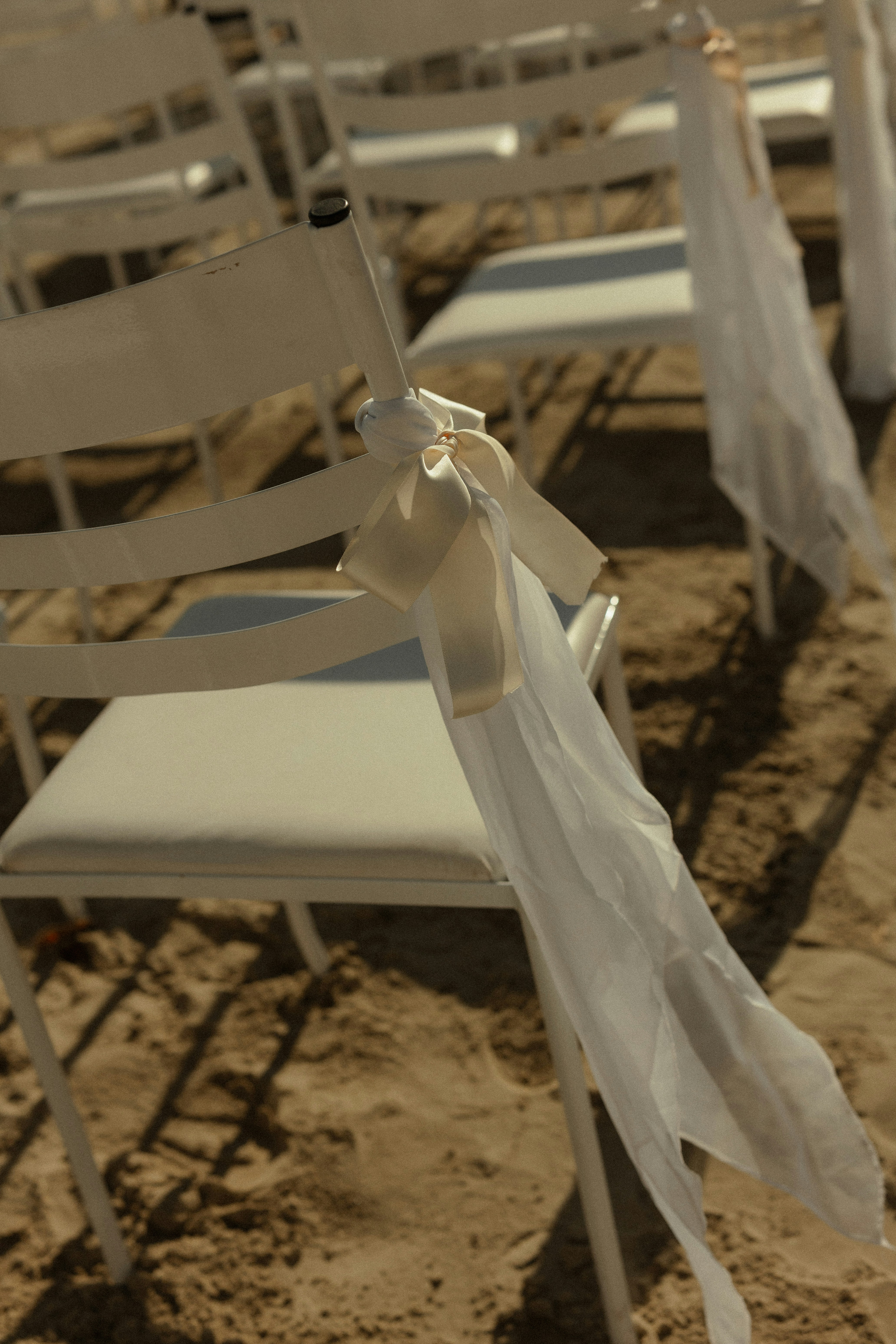 Rows of ceremony chairs on a sunlit beach with fabric accents
